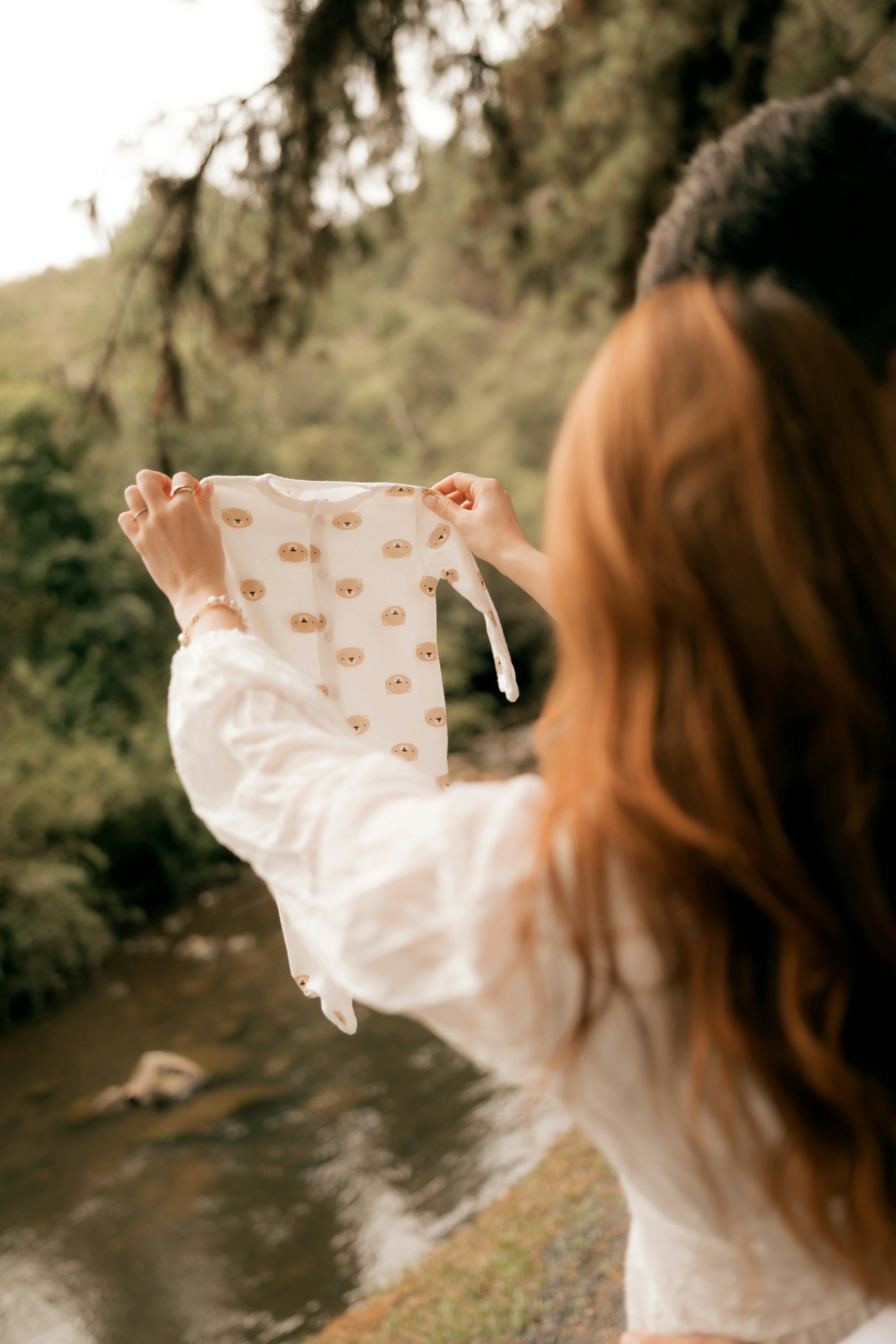 Fringe of a Moment: A woman raises a patterned fabric against a forested riverside