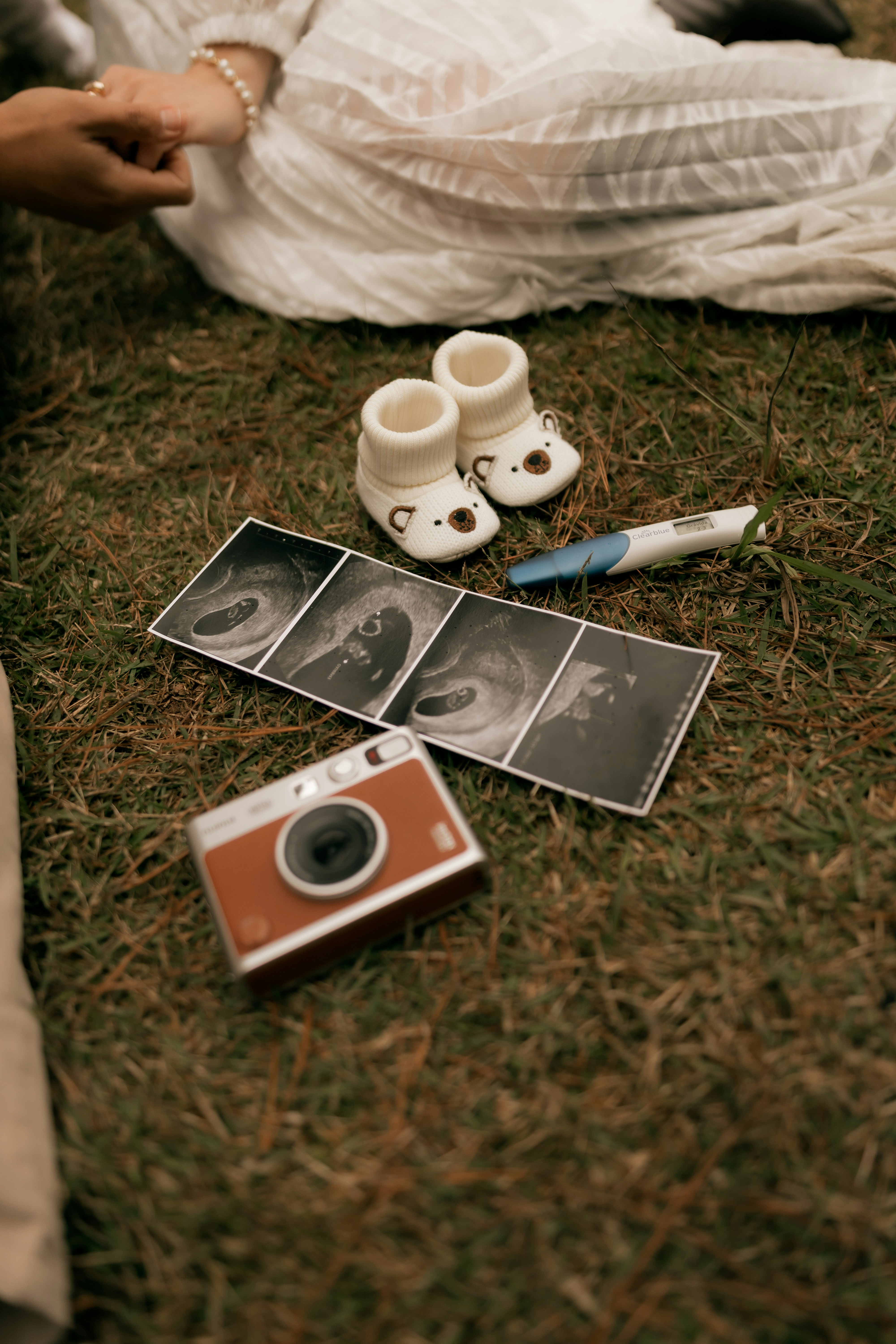 Baby booties, ultrasound photos, pregnancy test, and camera on grass.