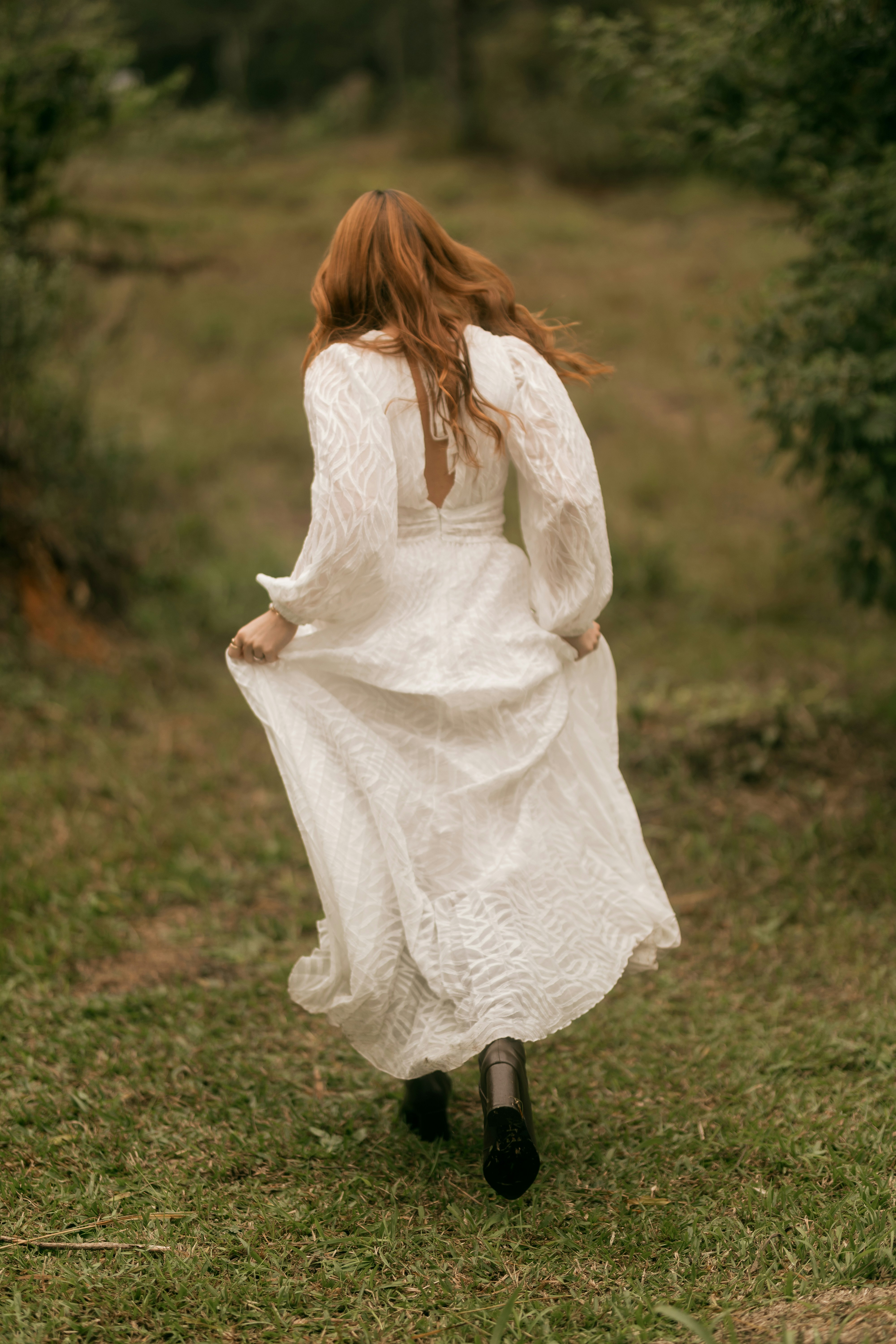 Red-haired woman in white dress walks away in nature.
