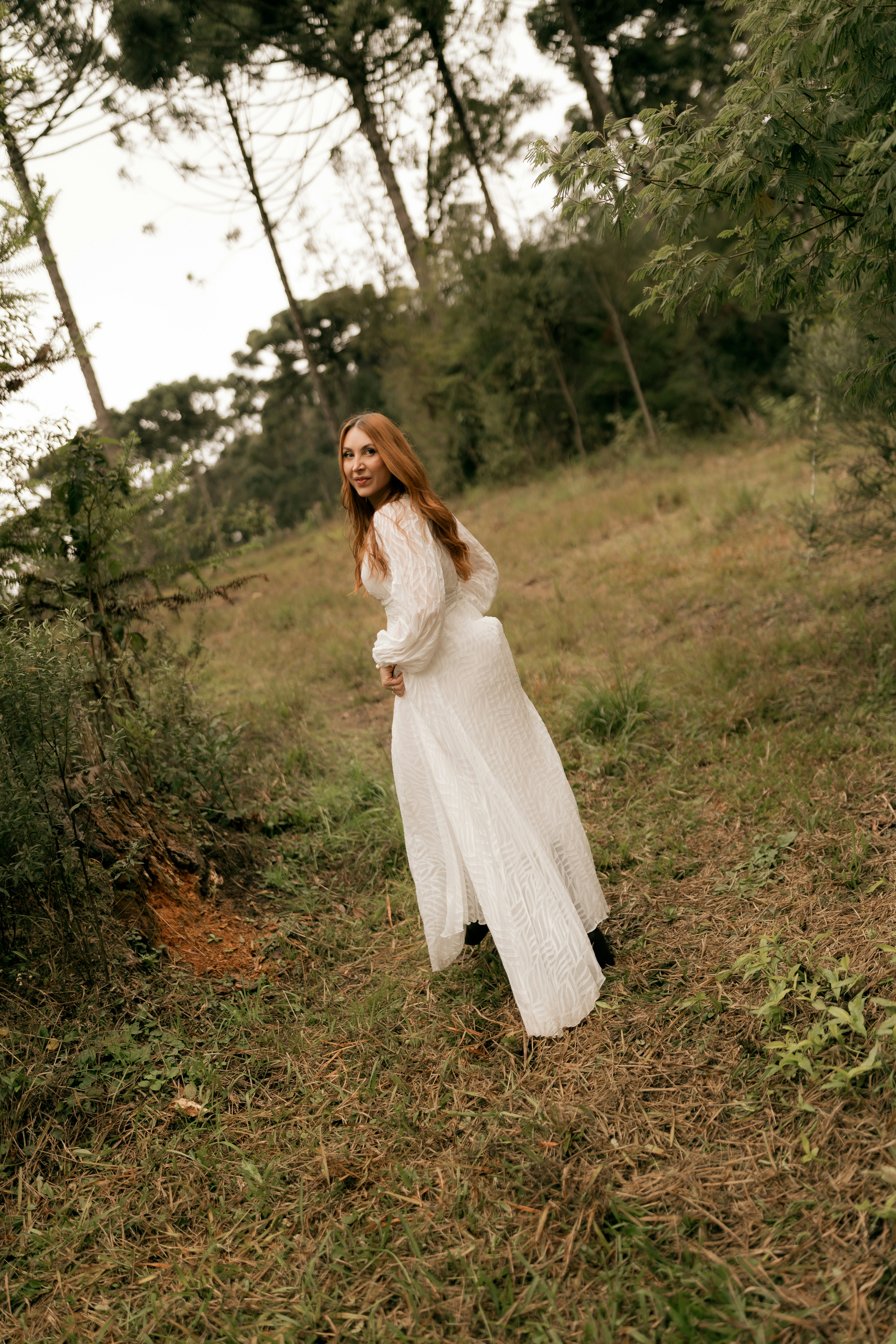 A woman in a white dress walking through a forest.
