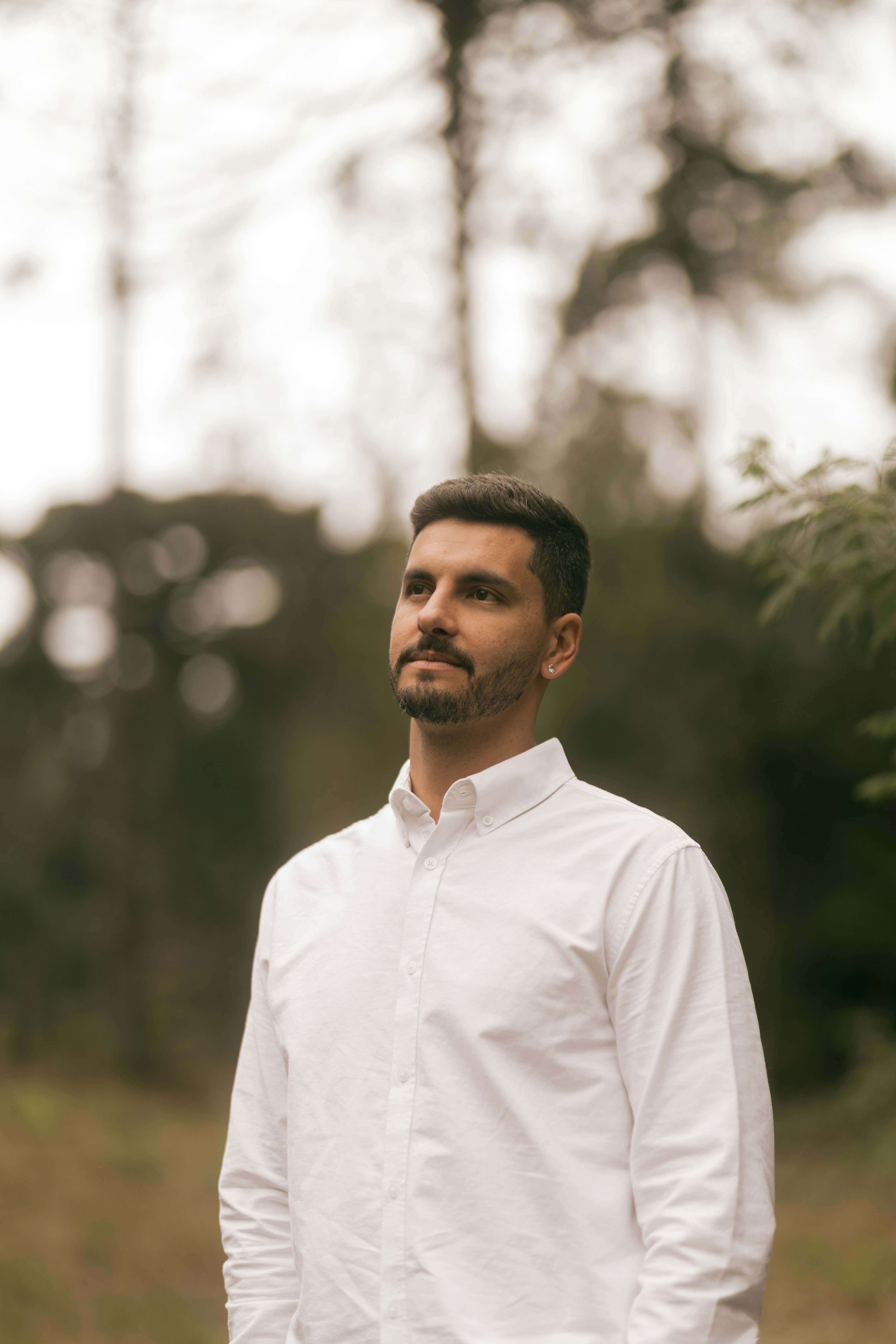 Bearded man in white shirt looking contemplatively in nature.