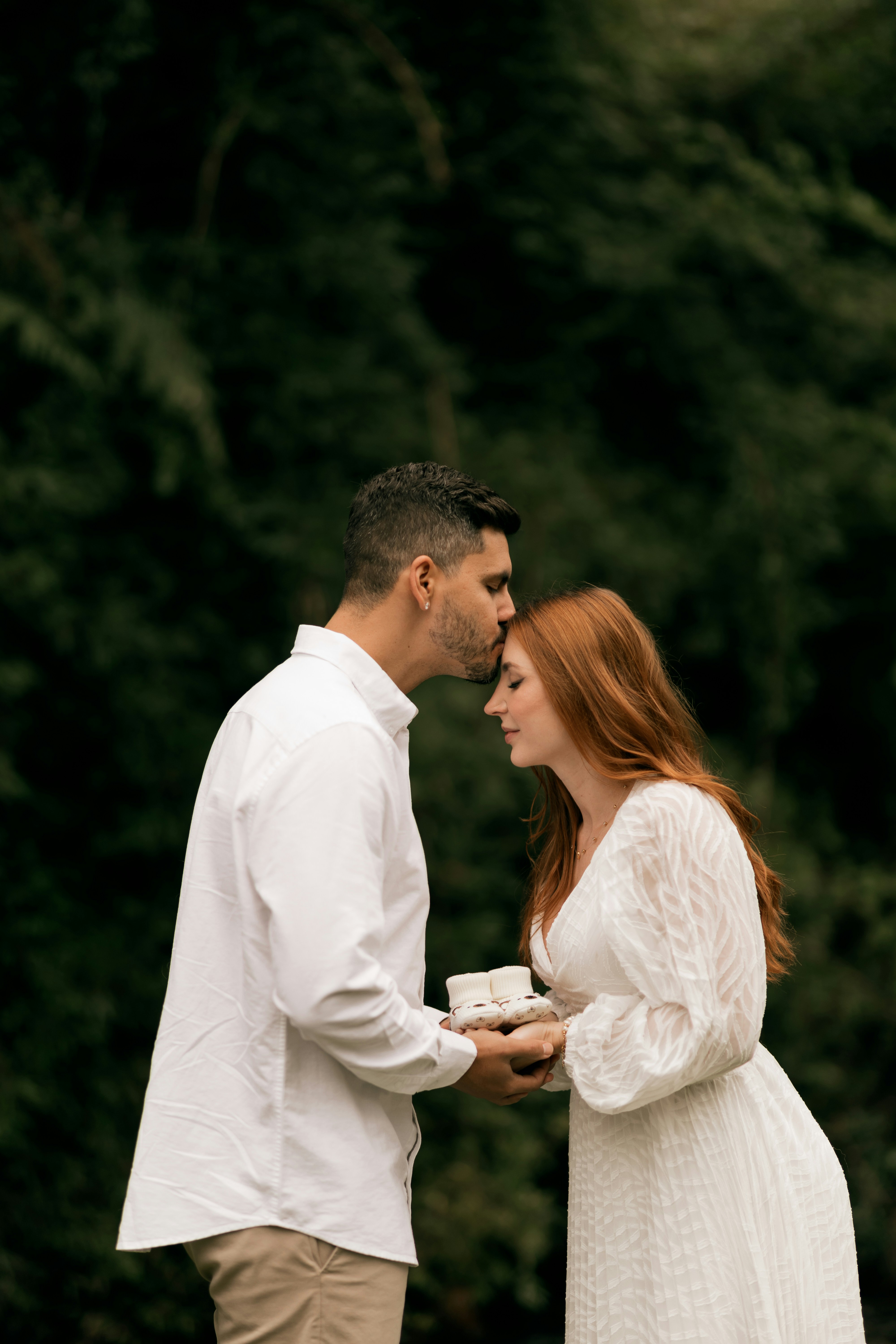A man kisses a woman's forehead, holding small white objects.