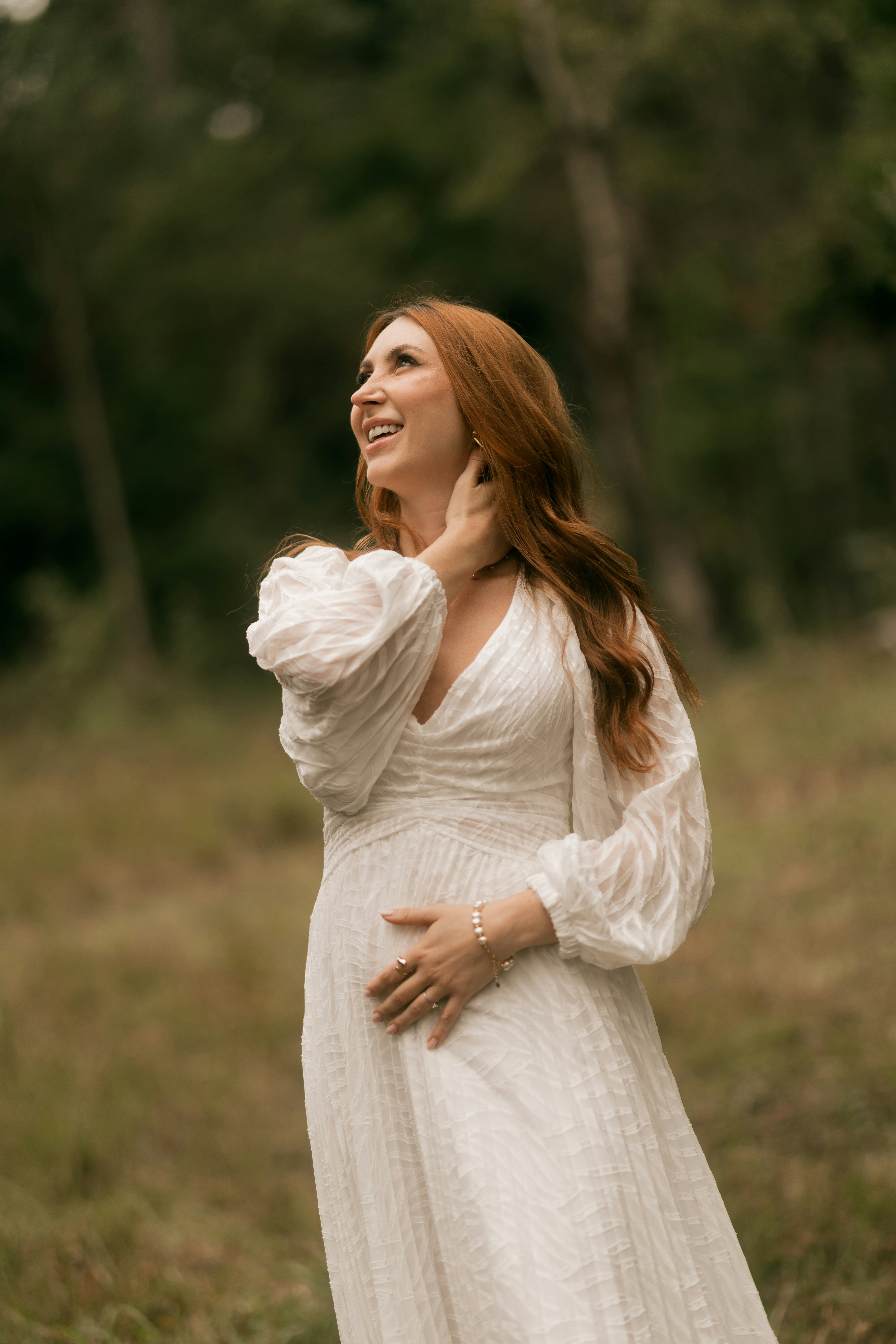 Red-haired woman in white dress smiling outdoors.
