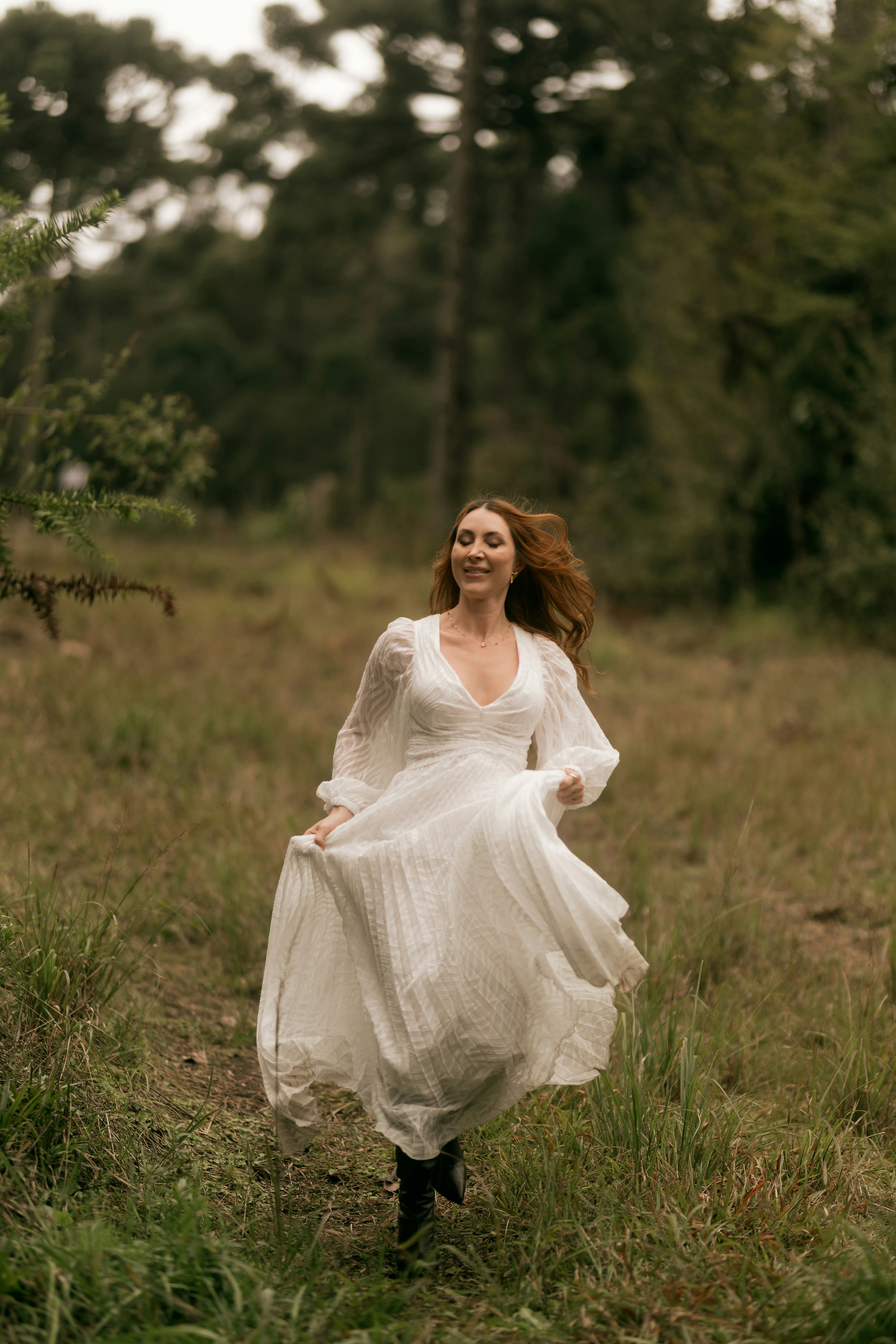Woman in flowing white dress running happily through a field.