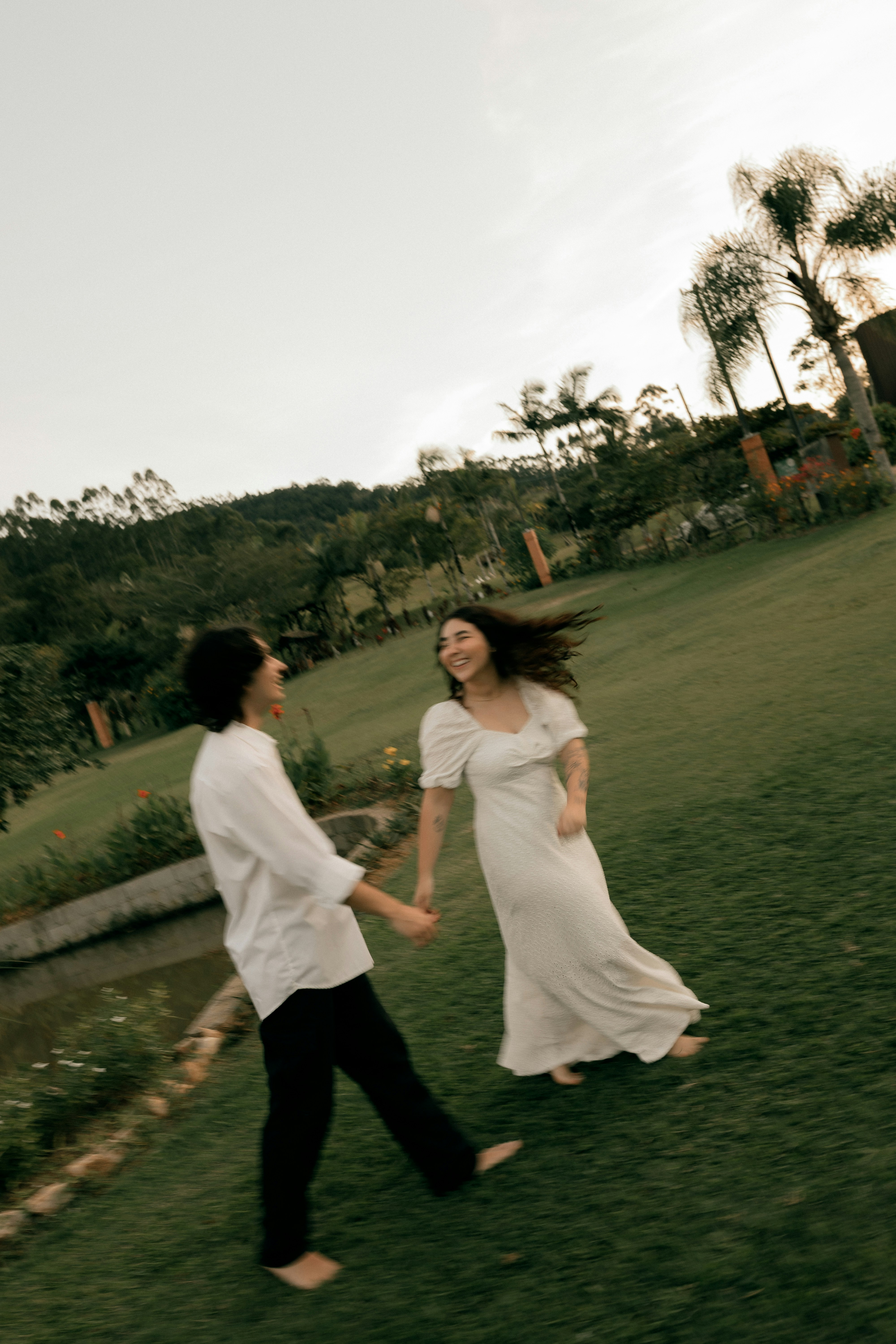 Two individuals holding hands, walking barefoot on green grass.