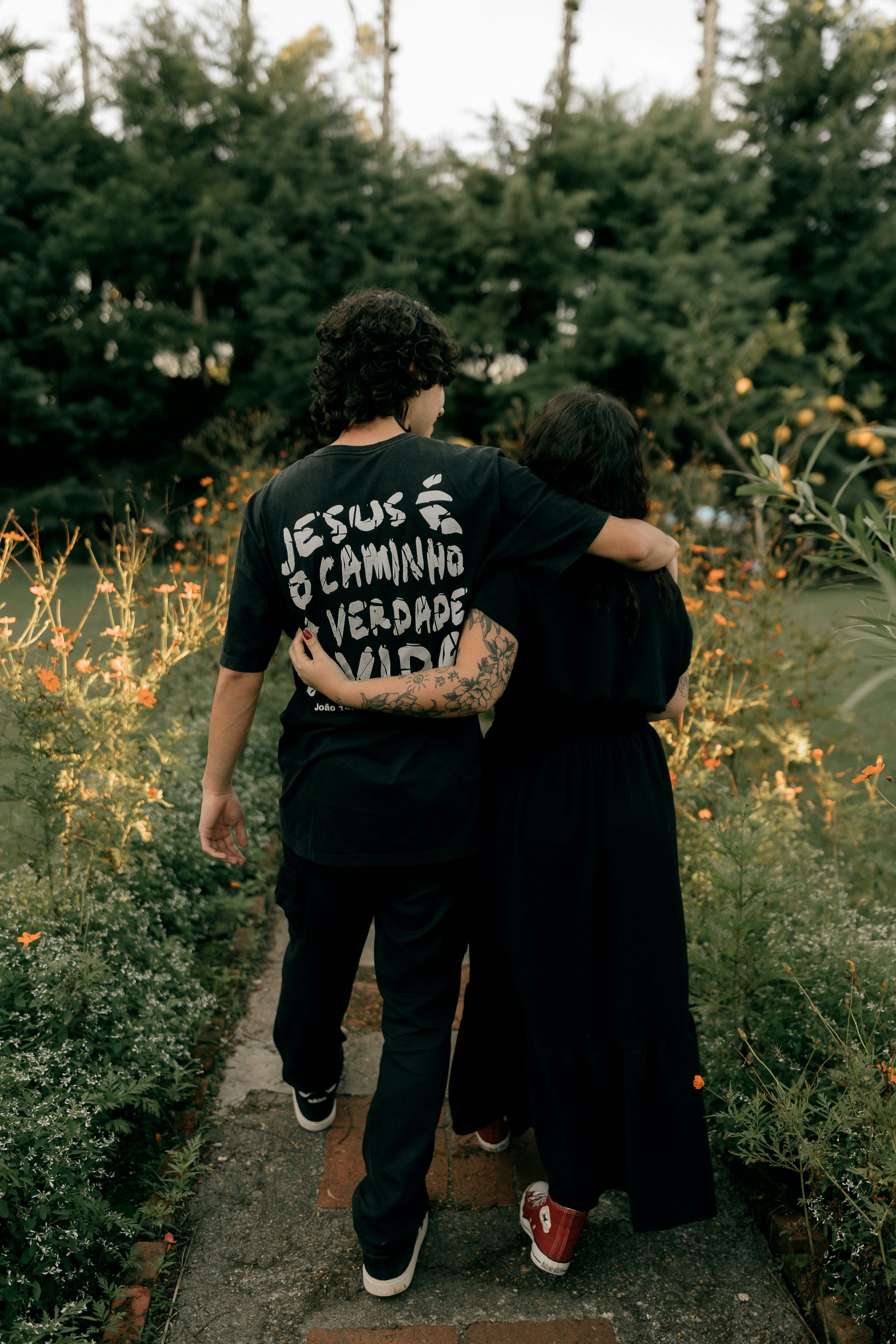 Two people walk arm-in-arm on a garden path.