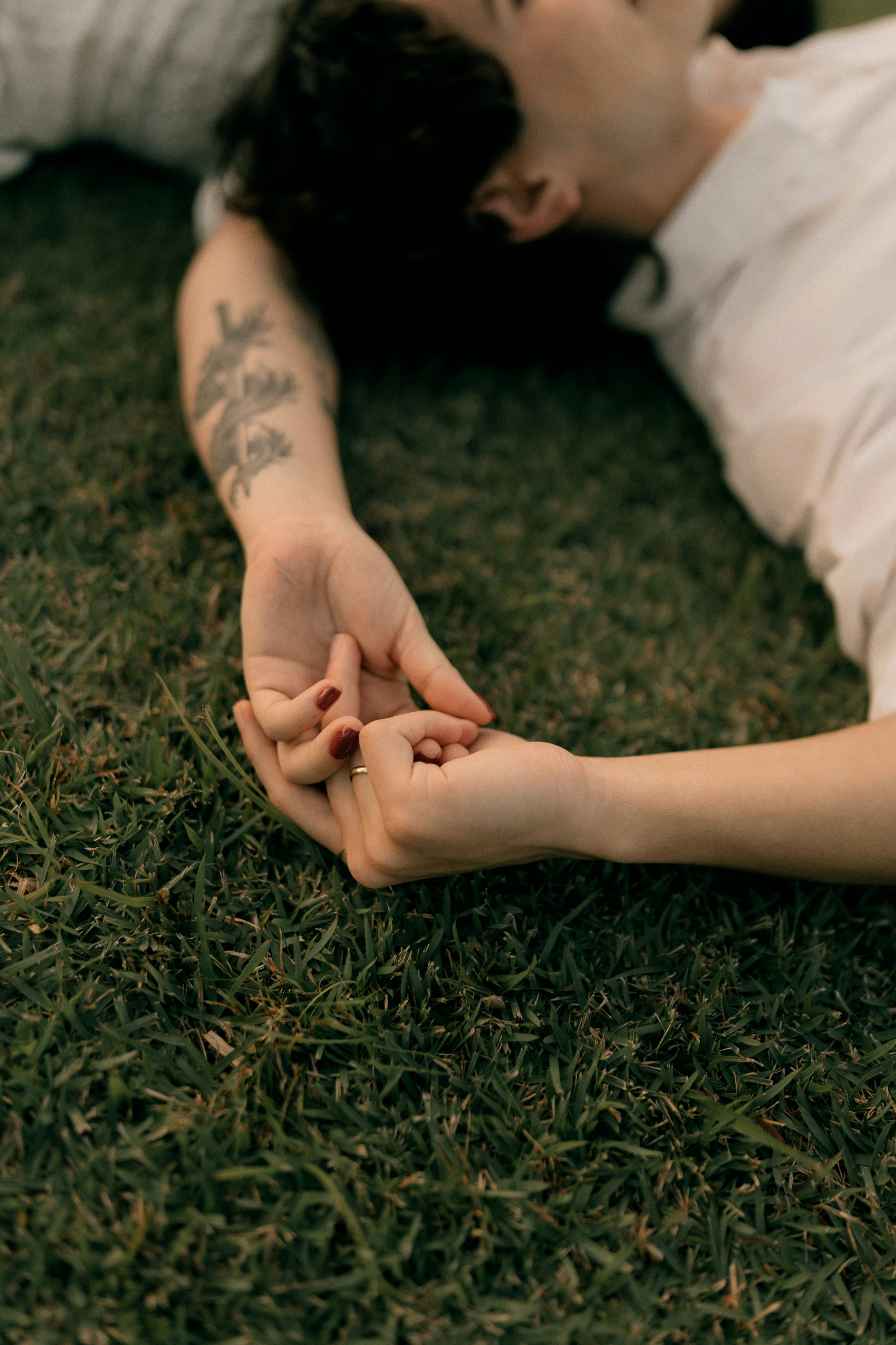 Two people's hands intertwined on green grass.