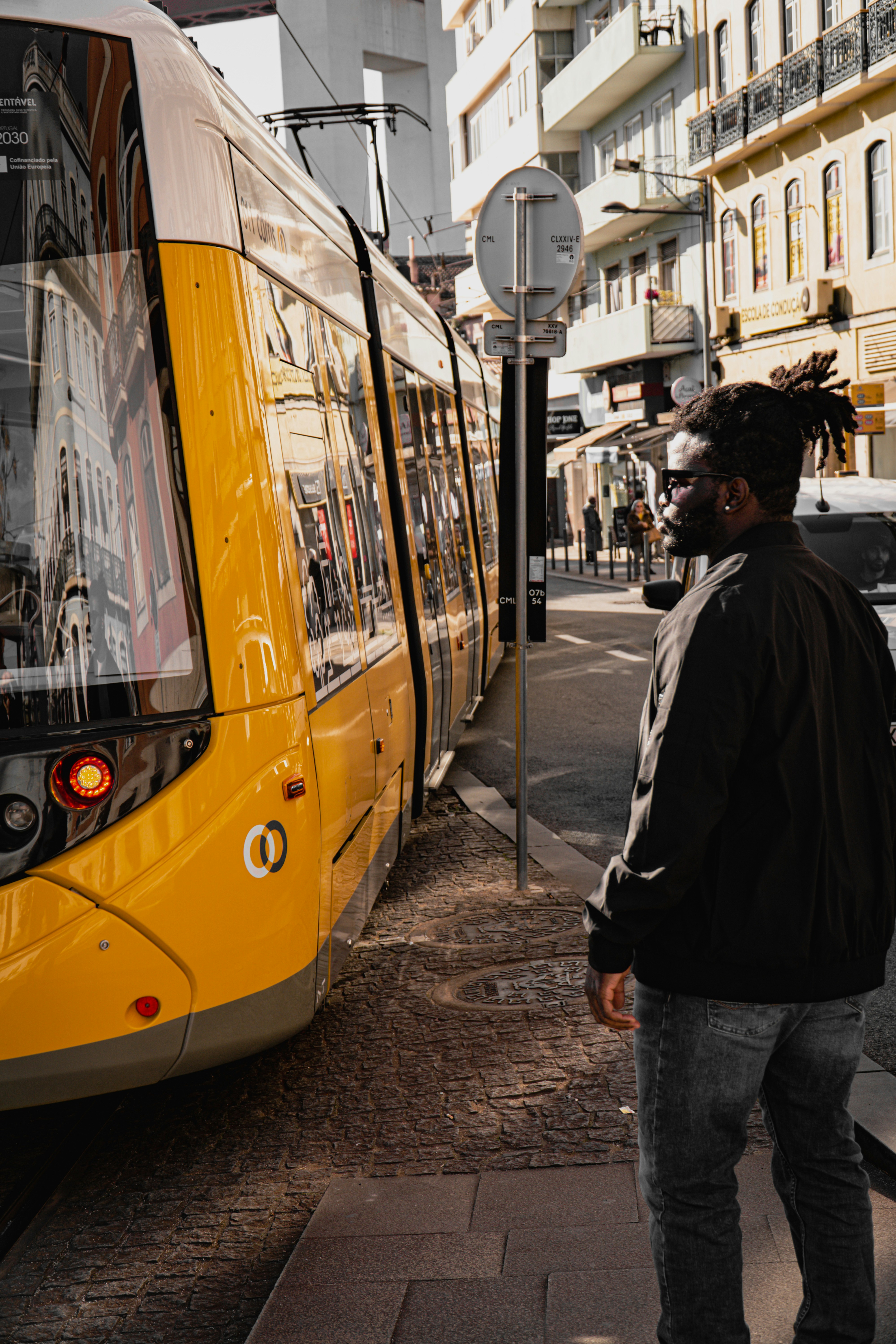 Yellow tram at a busy city stop, man waiting in the foreground