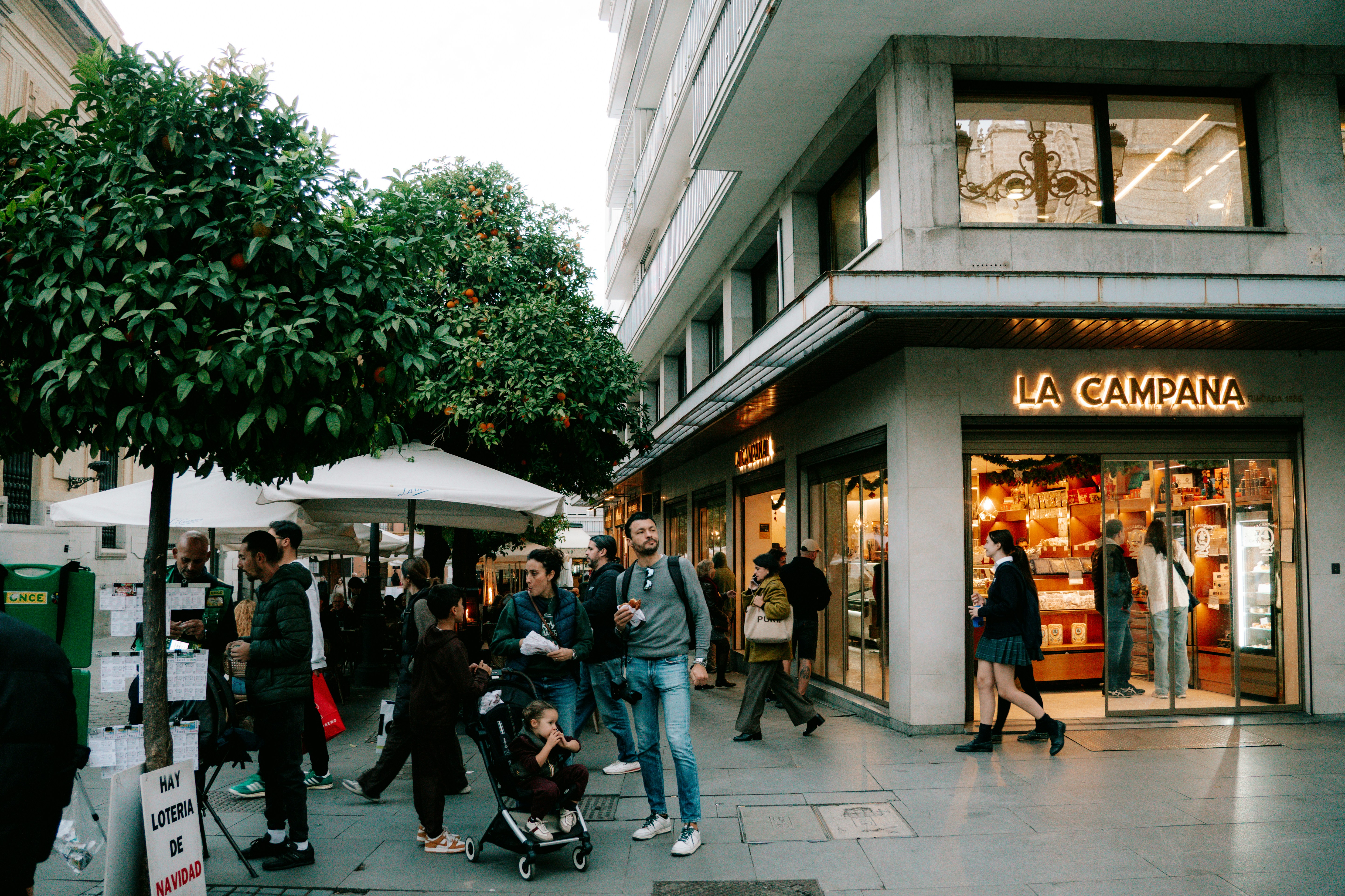 Street corner in front of La Campana: family, shoppers, and a pastry shop collide in urban life
