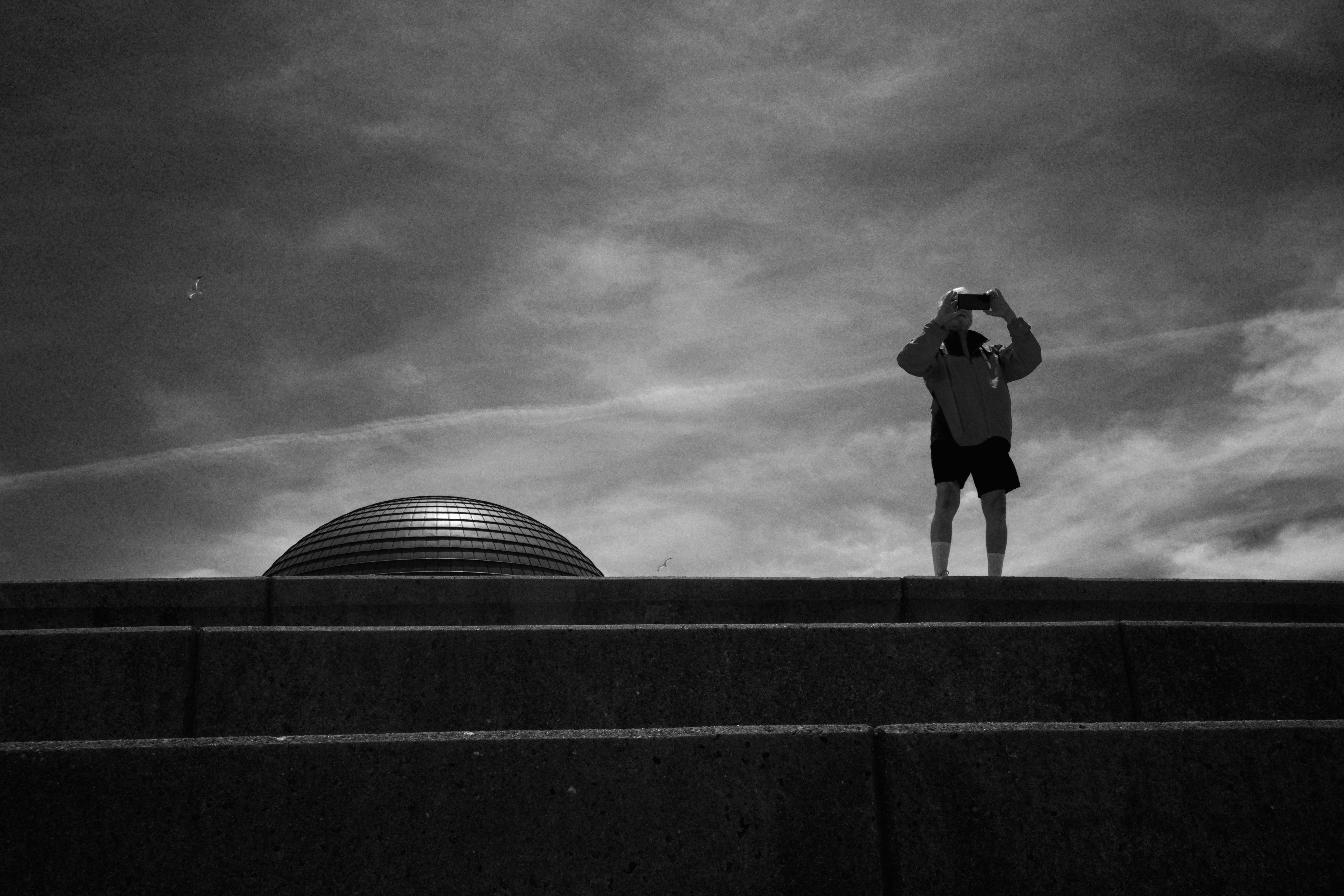 Barefoot person on wall with dome against cloudy sky.