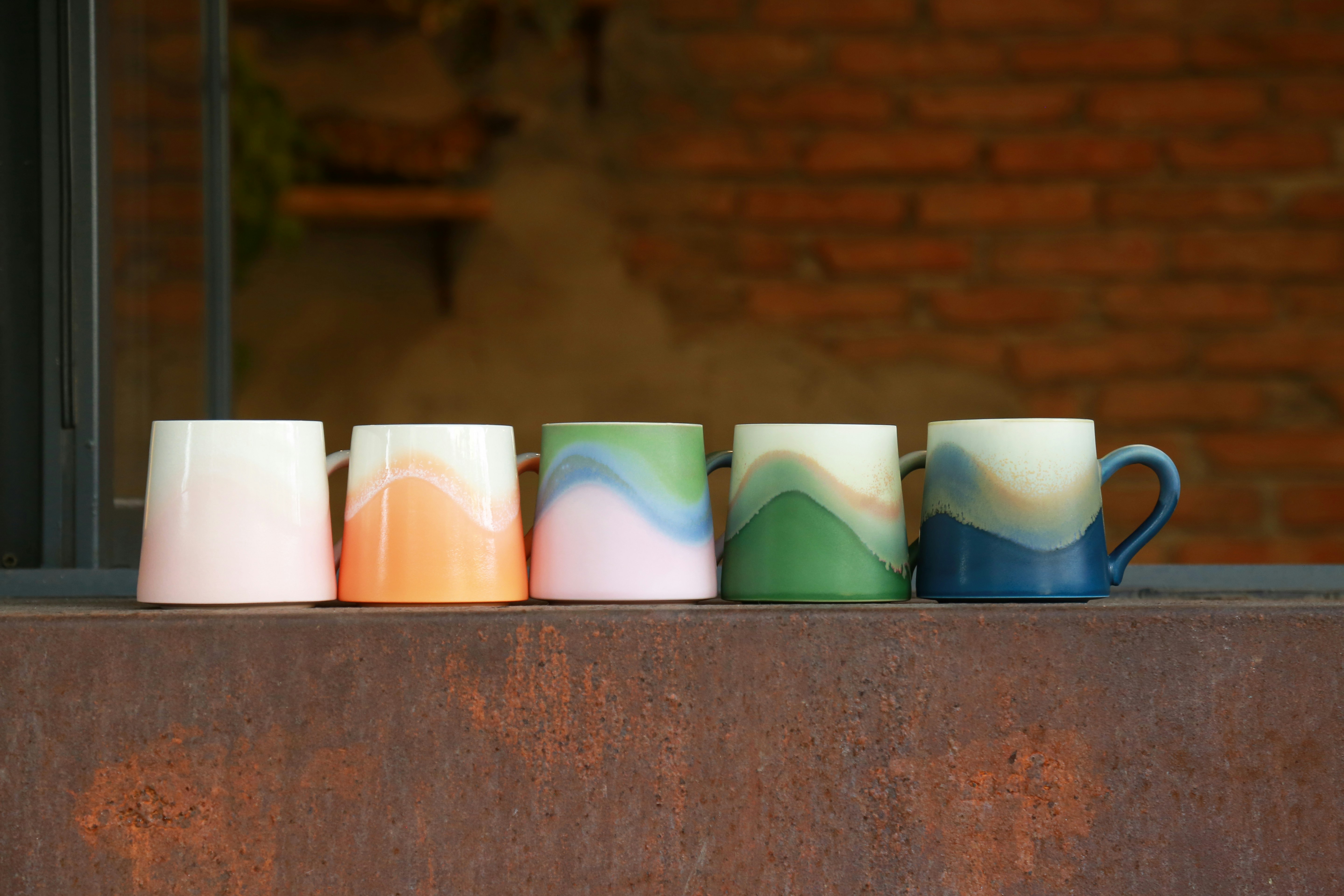 Colorful ceramic mugs resting on a rusted ledge beneath a window