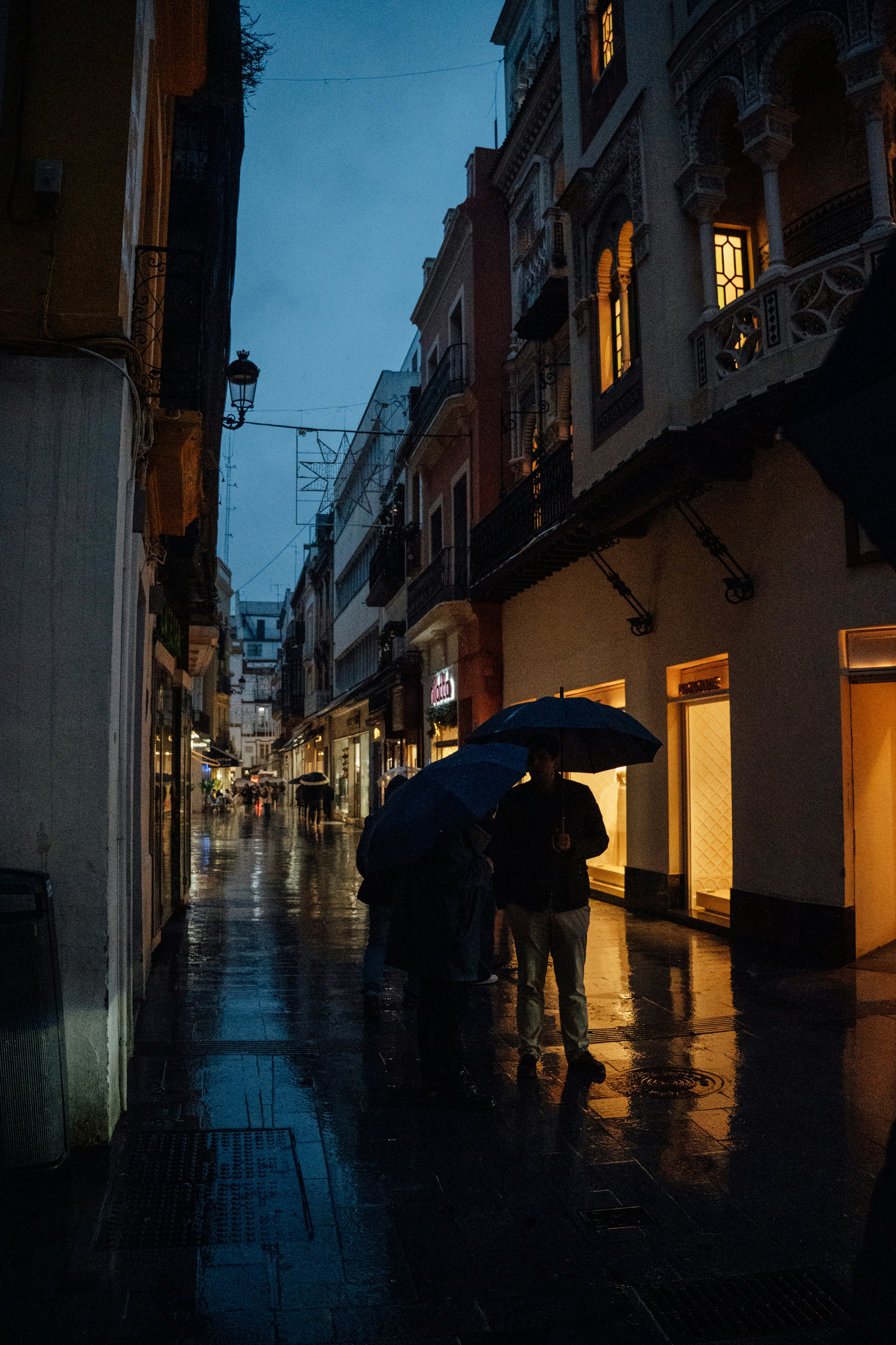 Rainy Callejón: Neon Glow and Umbrellas in a Narrow City Street