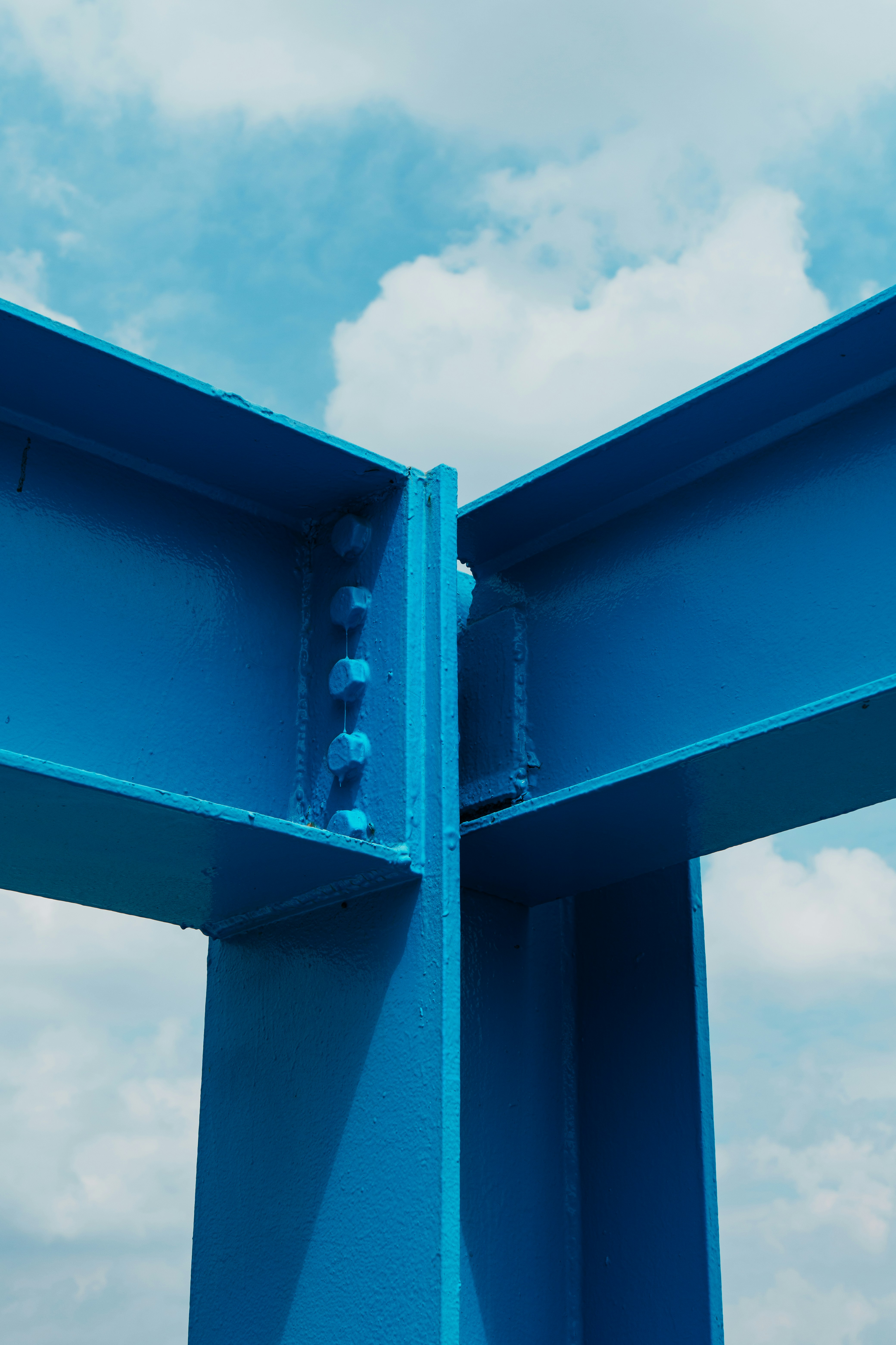 Bright blue structural steel beams against a cloudy sky.