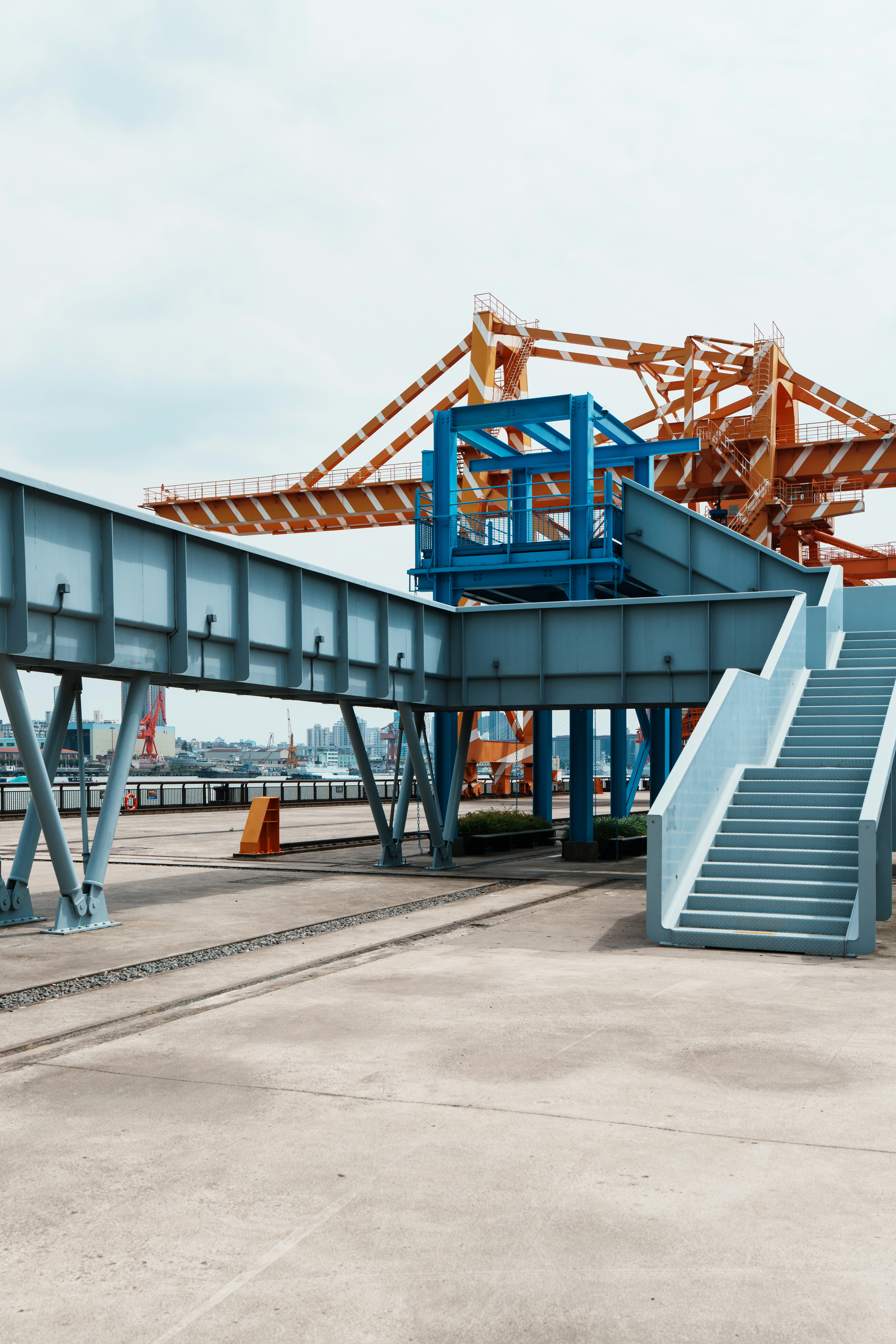 Industrial port with blue walkway, stairs, and large orange cranes.