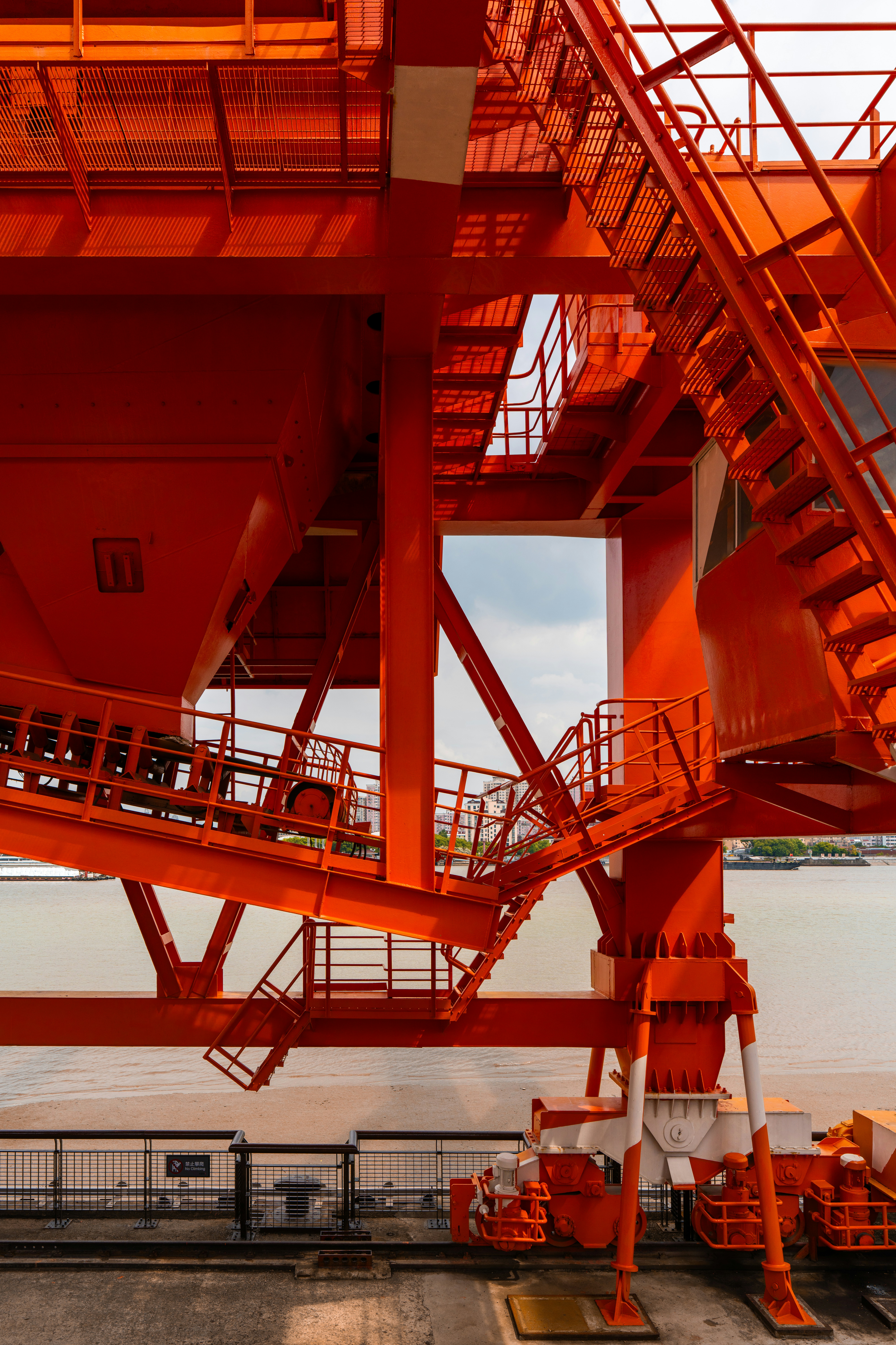 Bright orange industrial machinery with stairs by a river.