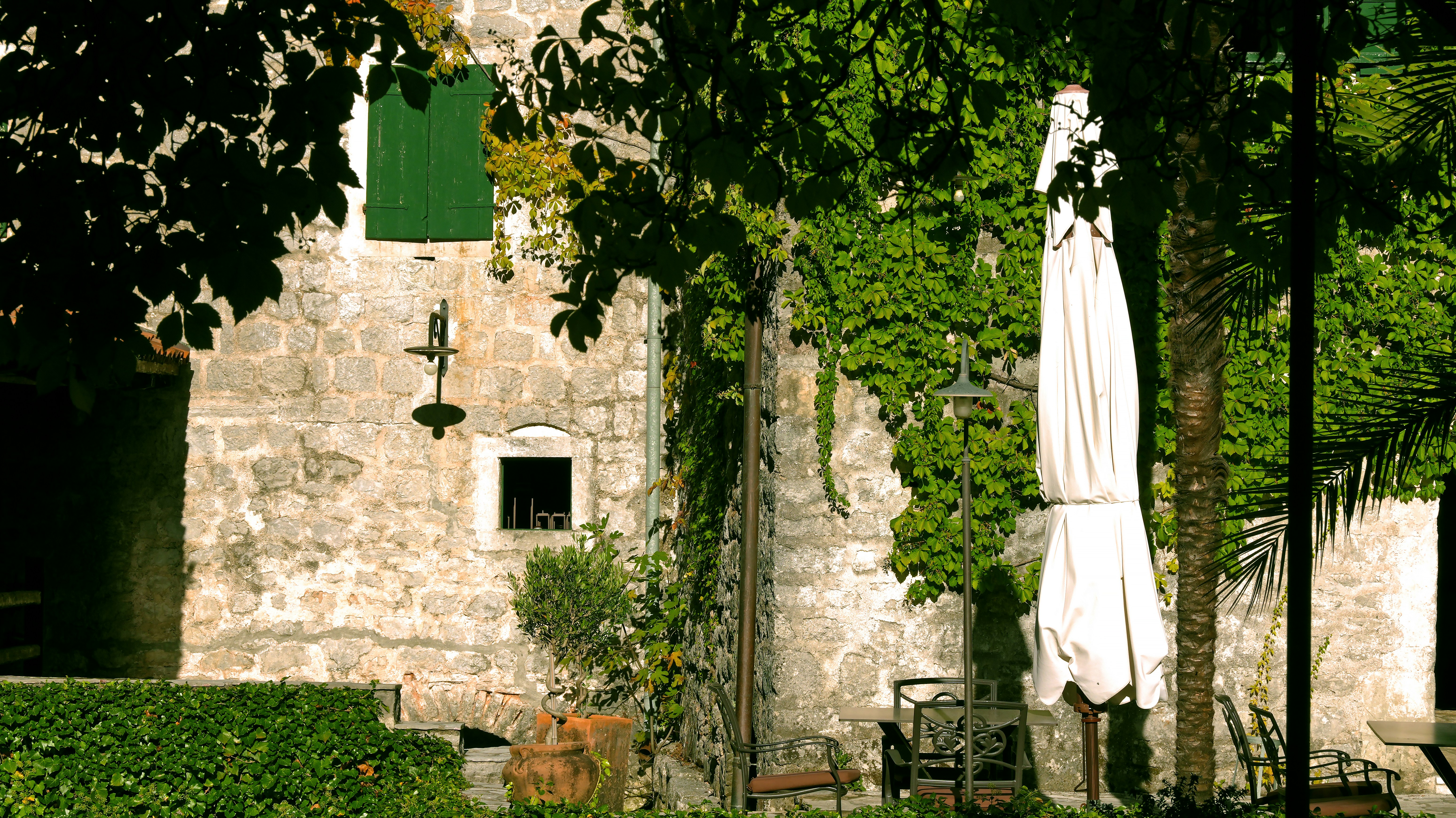 Sunlit Stone Terrace with Greenery and Closed Parasol