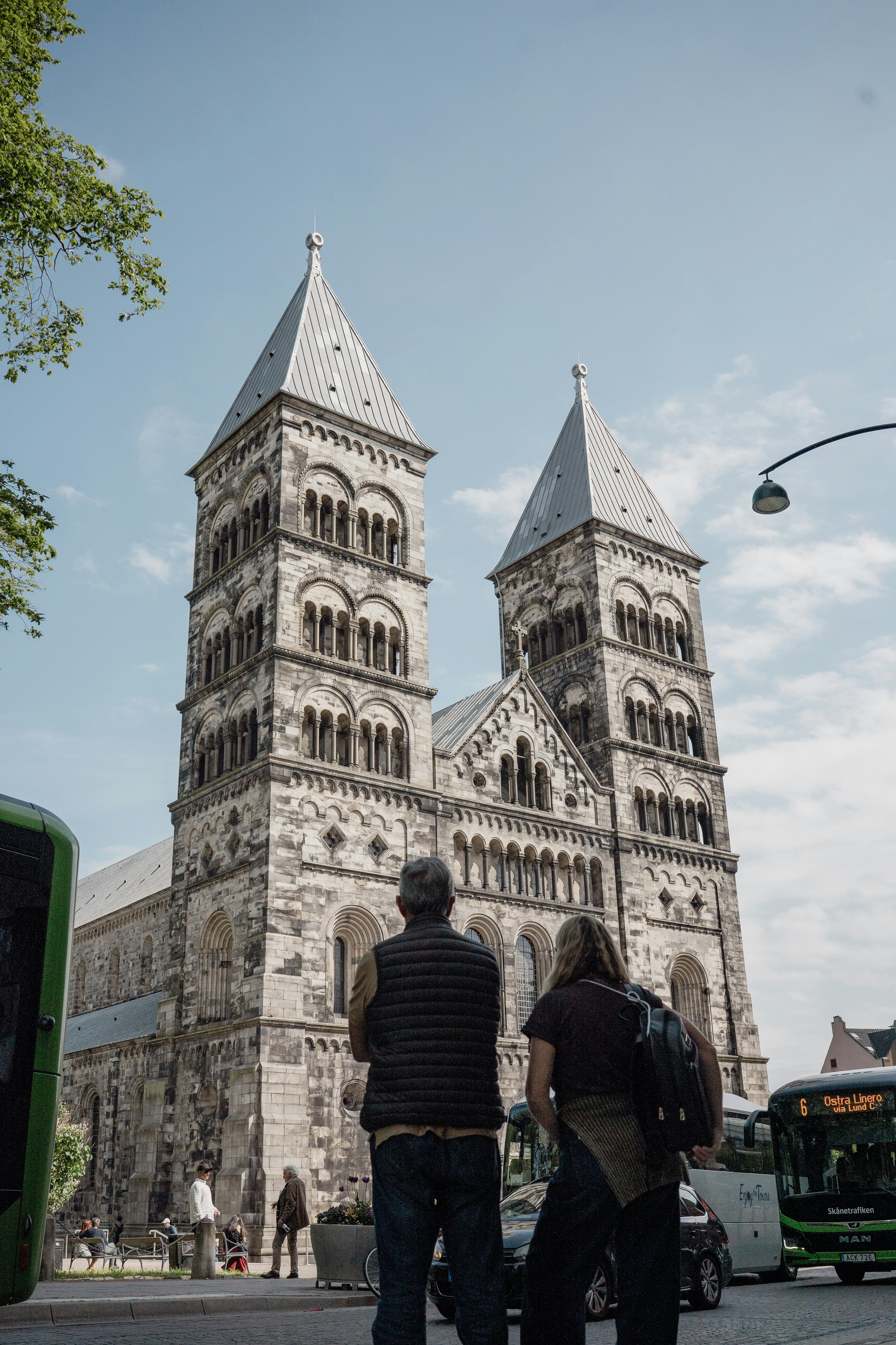 Two Tourists Observe a Romanesque Cathedral from a Busy Street