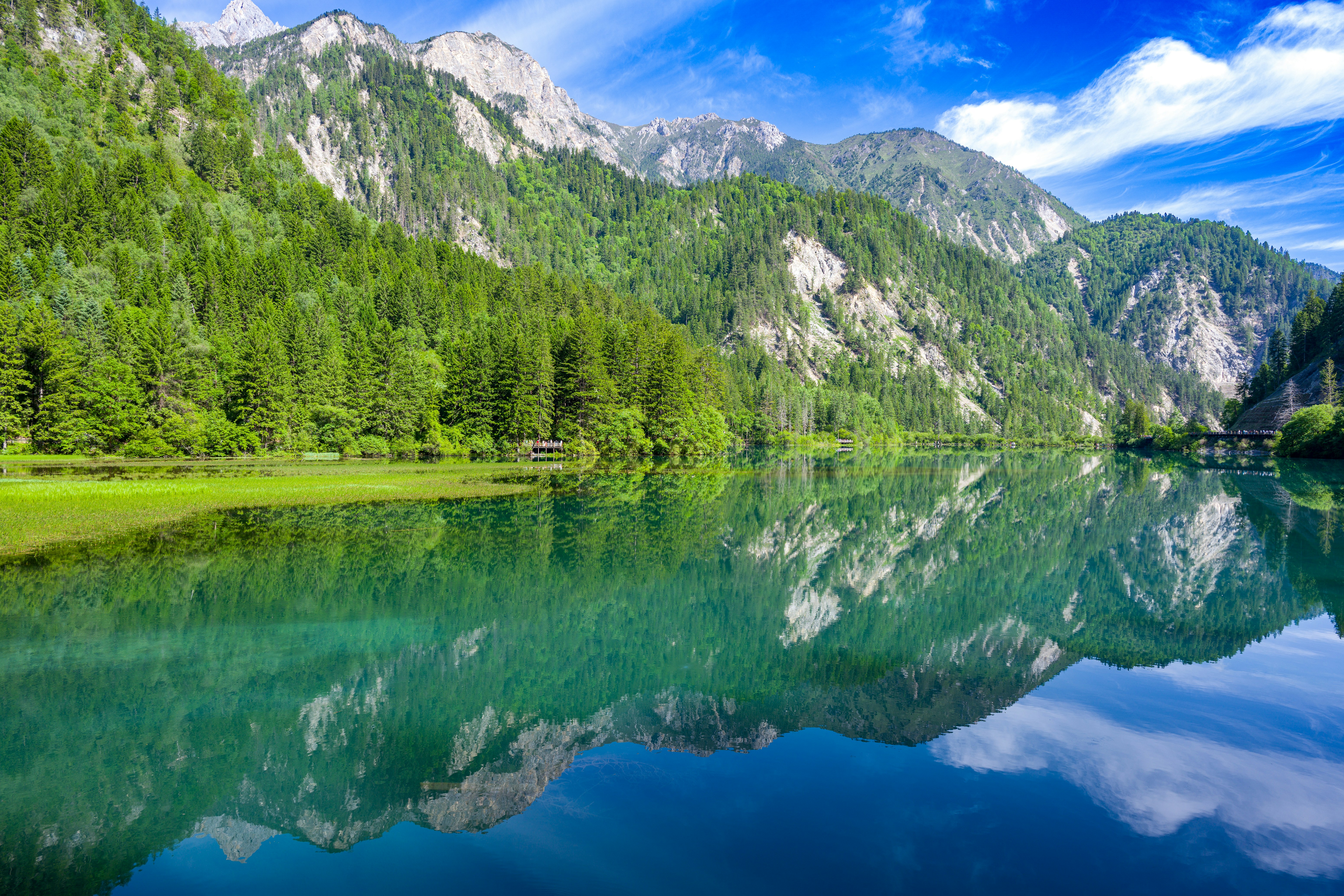 Alpine lake mirrors majestic mountains and vibrant green forests.