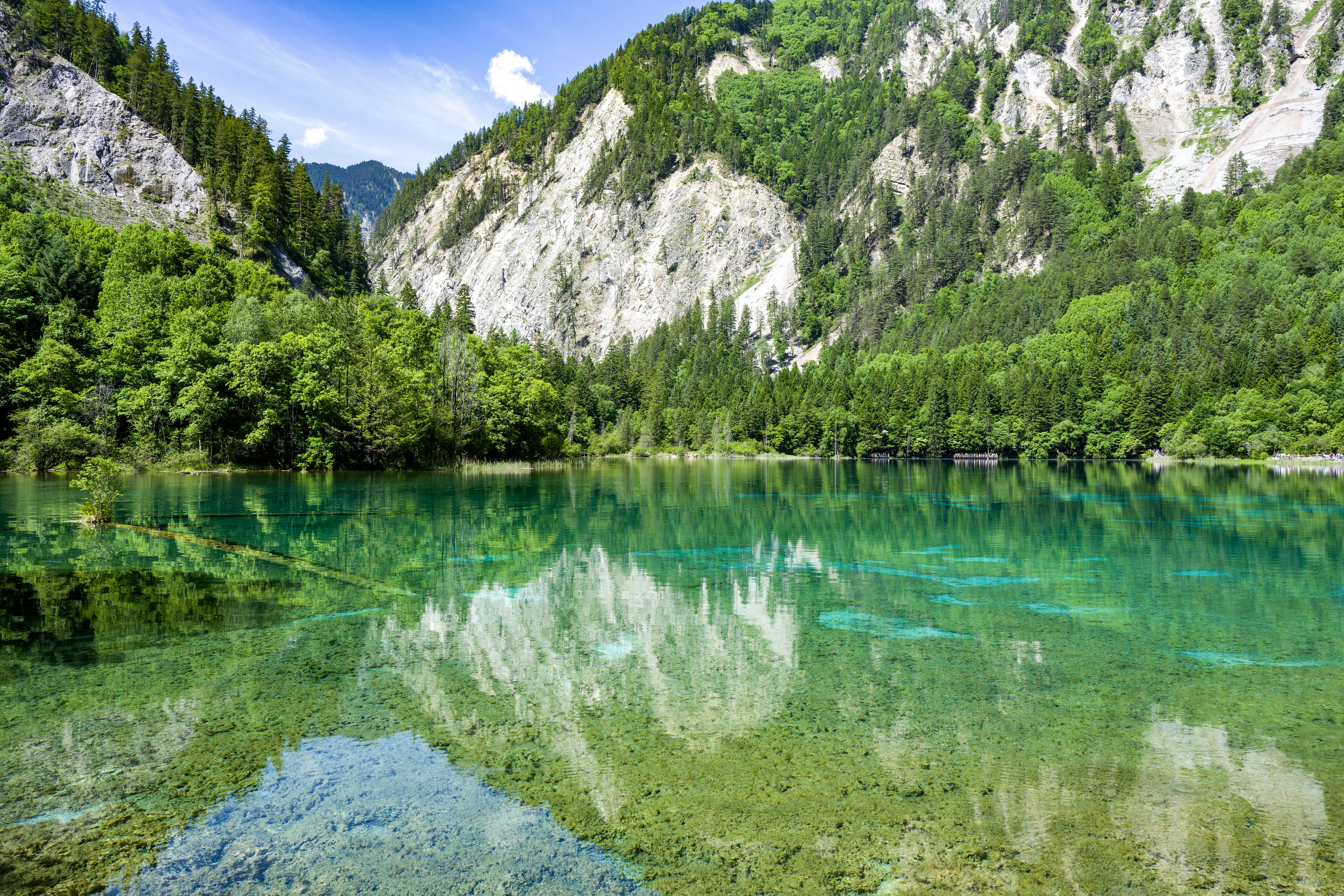 Clear turquoise lake reflects green mountains and blue sky.