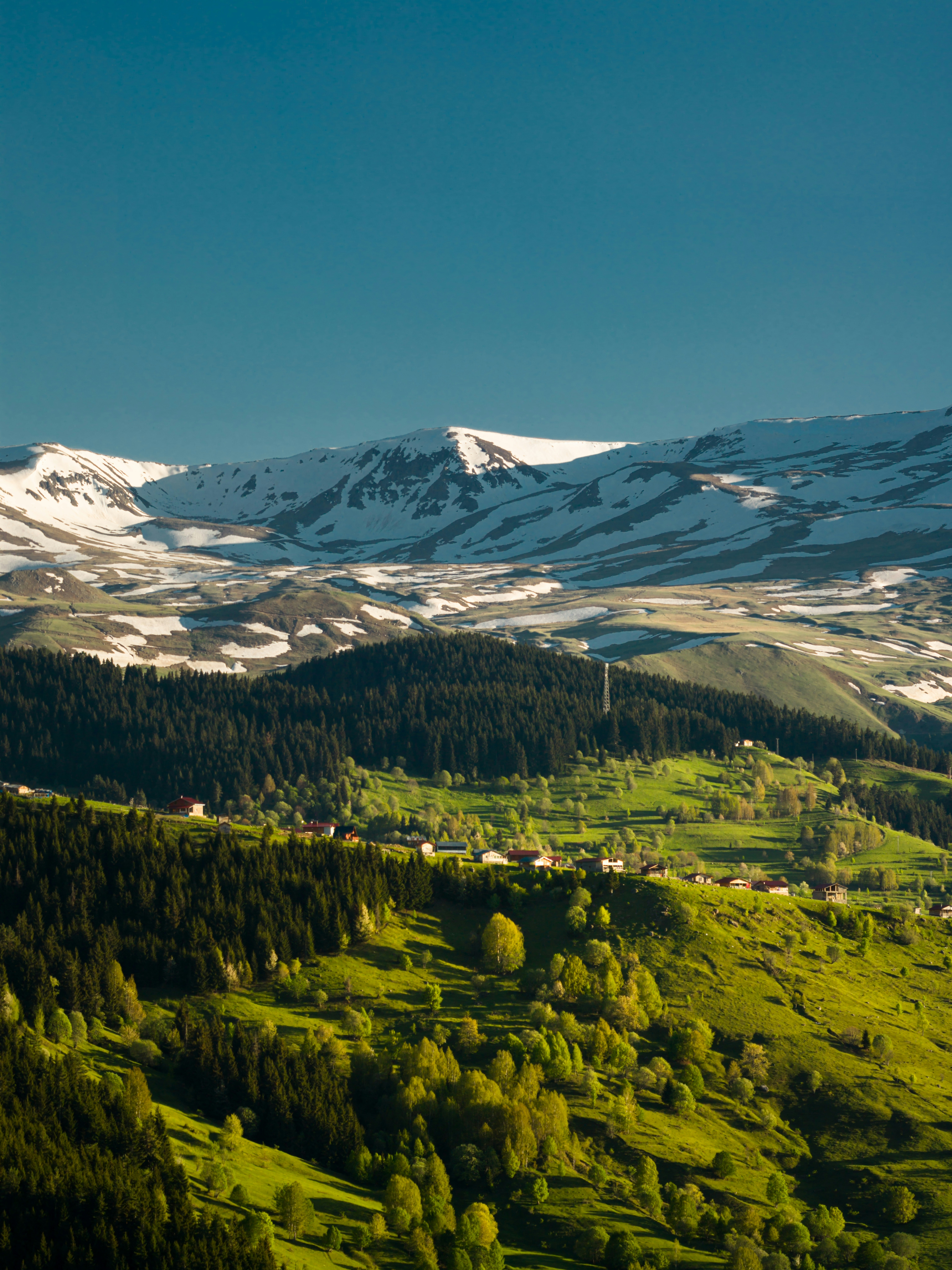 Snow-capped mountains overlook a green valley with a village.
