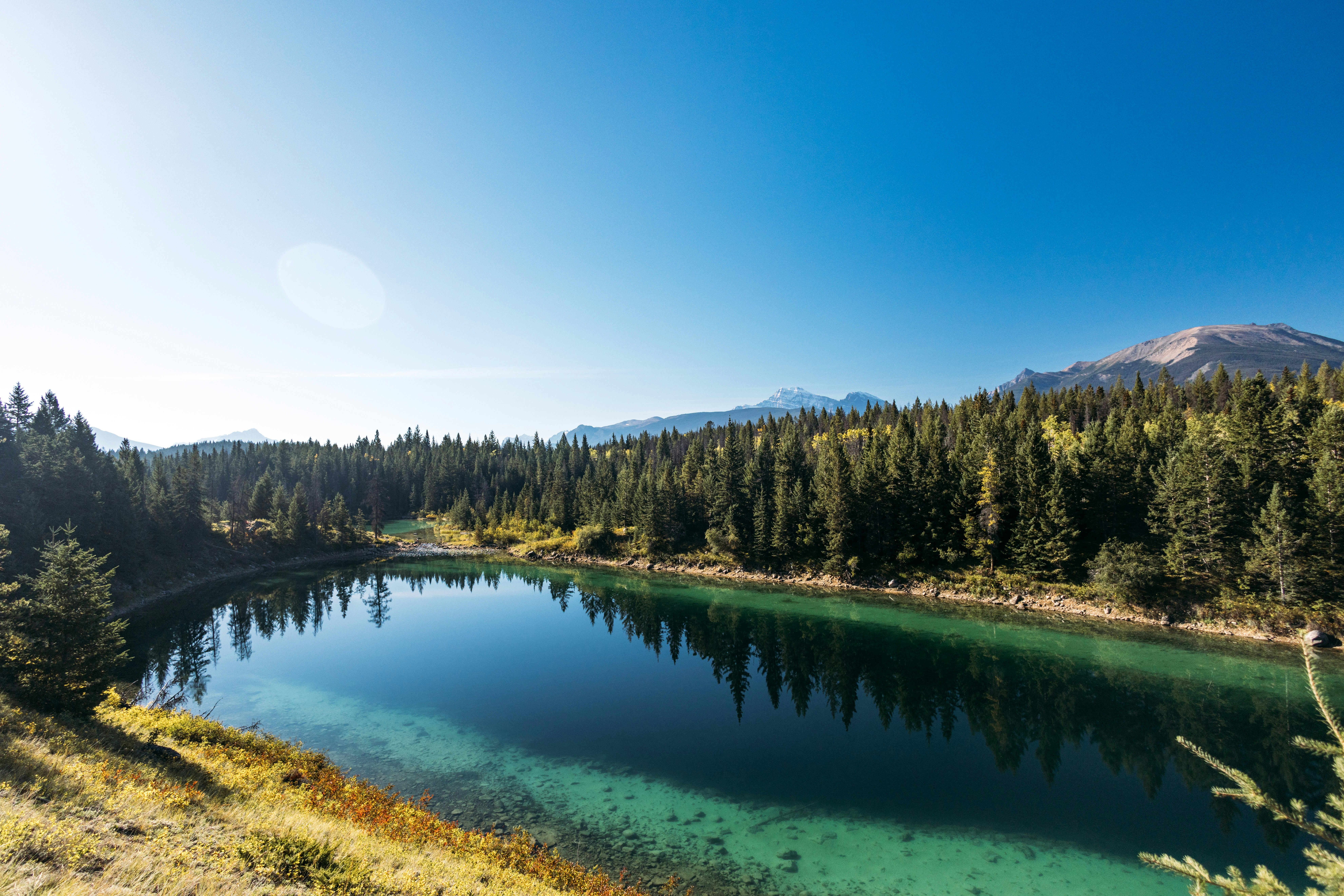 A clear blue-green lake surrounded by pine forests and mountains.