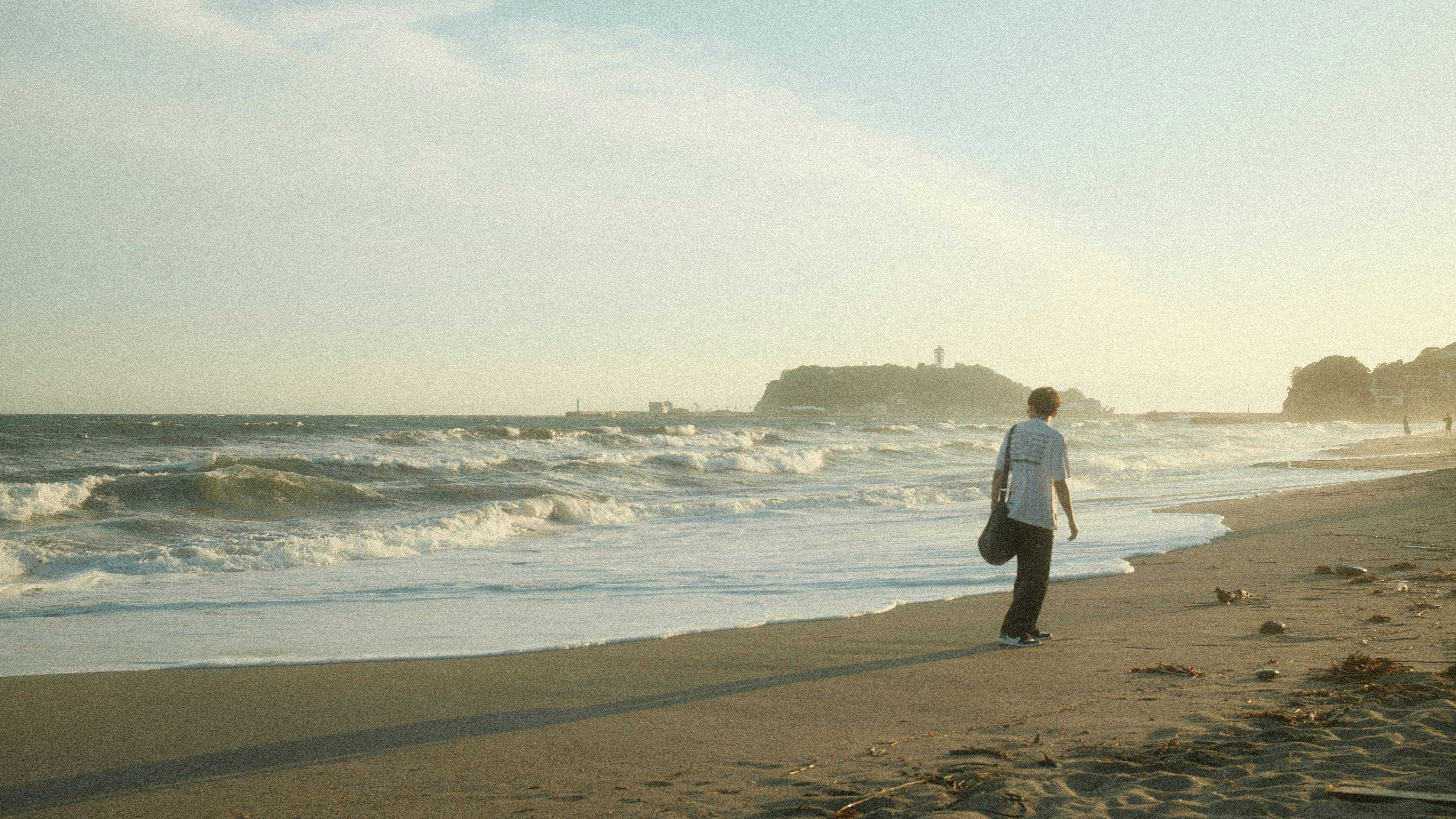 Person walks on sandy beach with ocean waves at sunset.