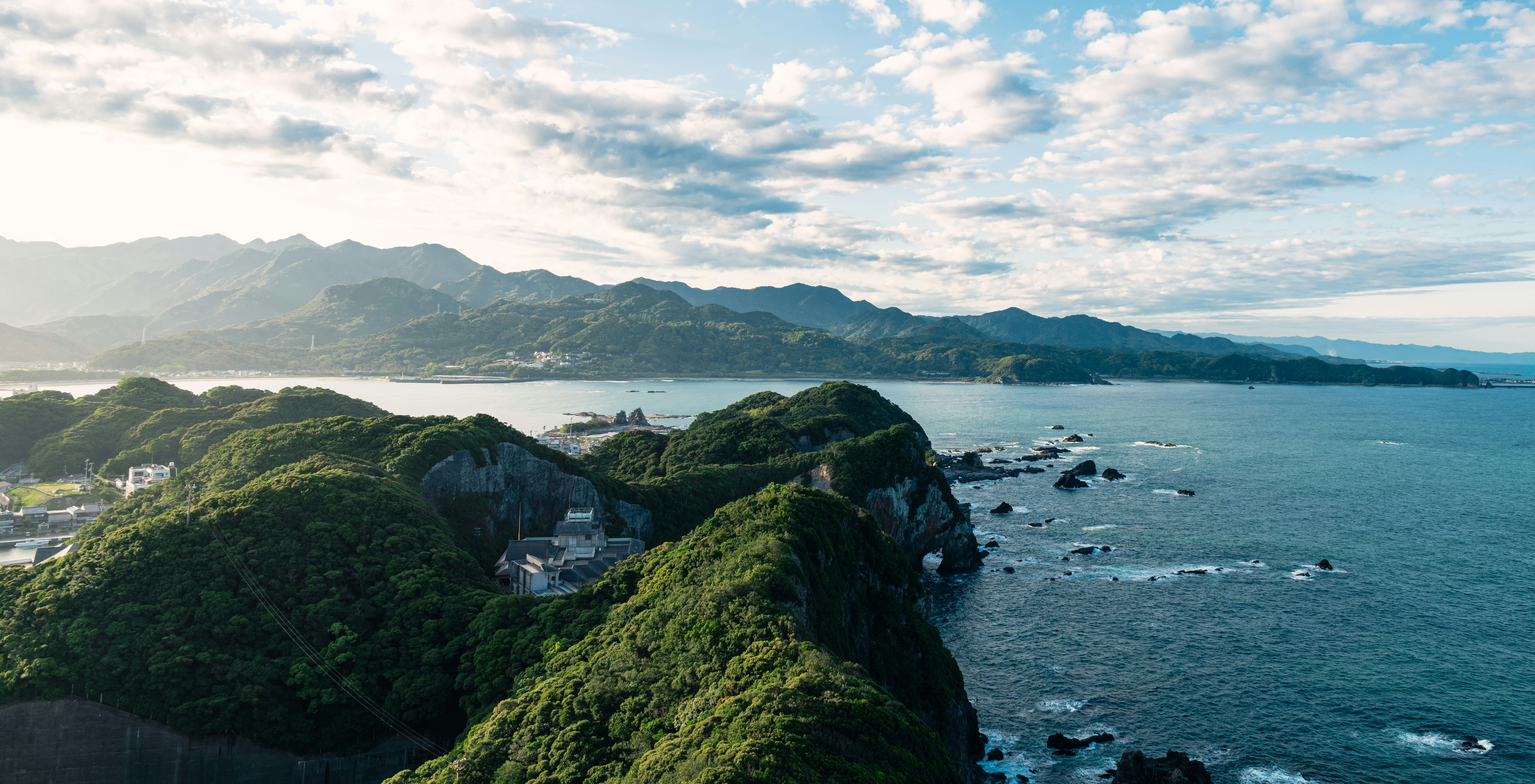 Coastal Ribbon: Green Cliffs and Distant Peaks Over Turquoise Sea