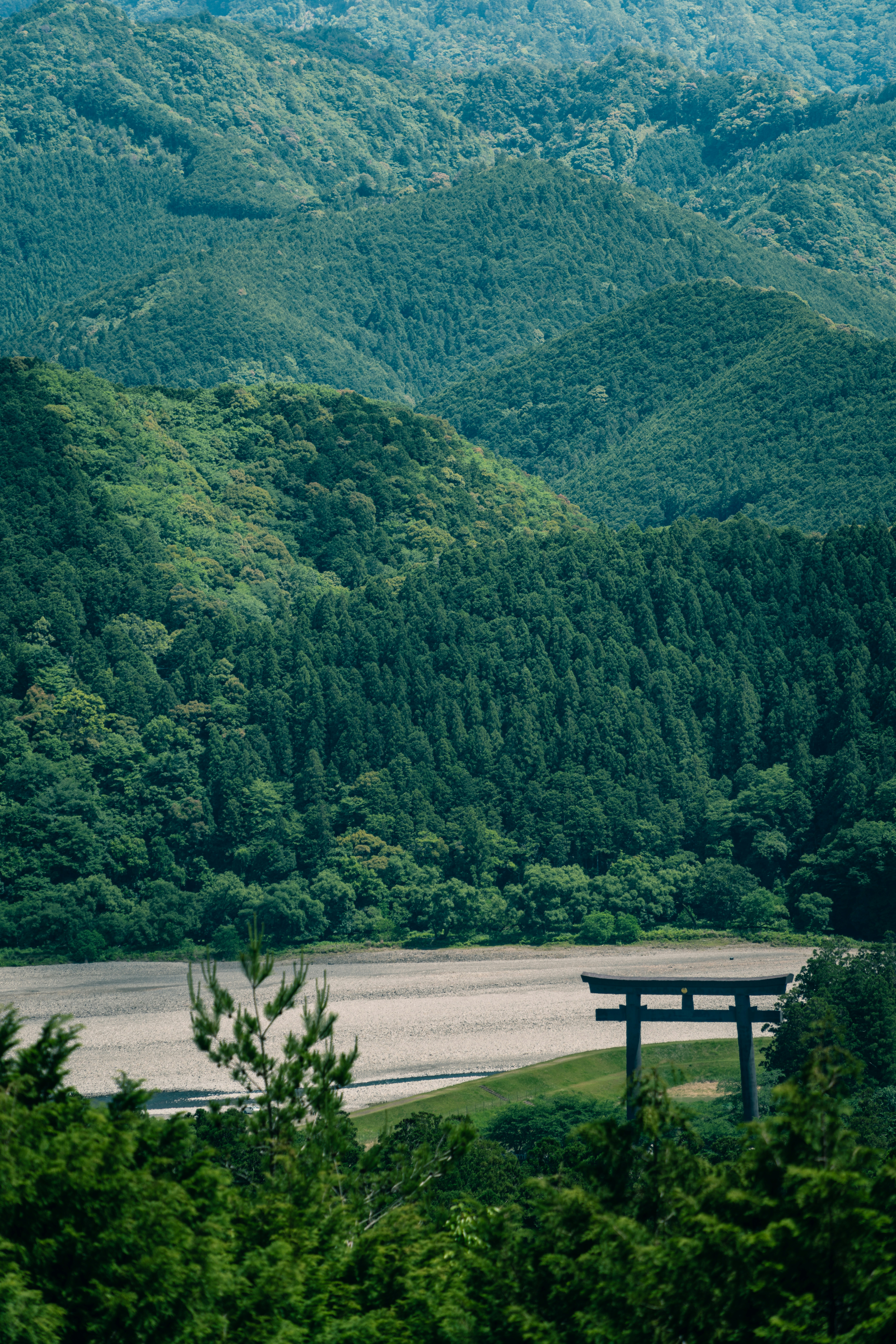 A torii gate by a lake with lush green mountains.