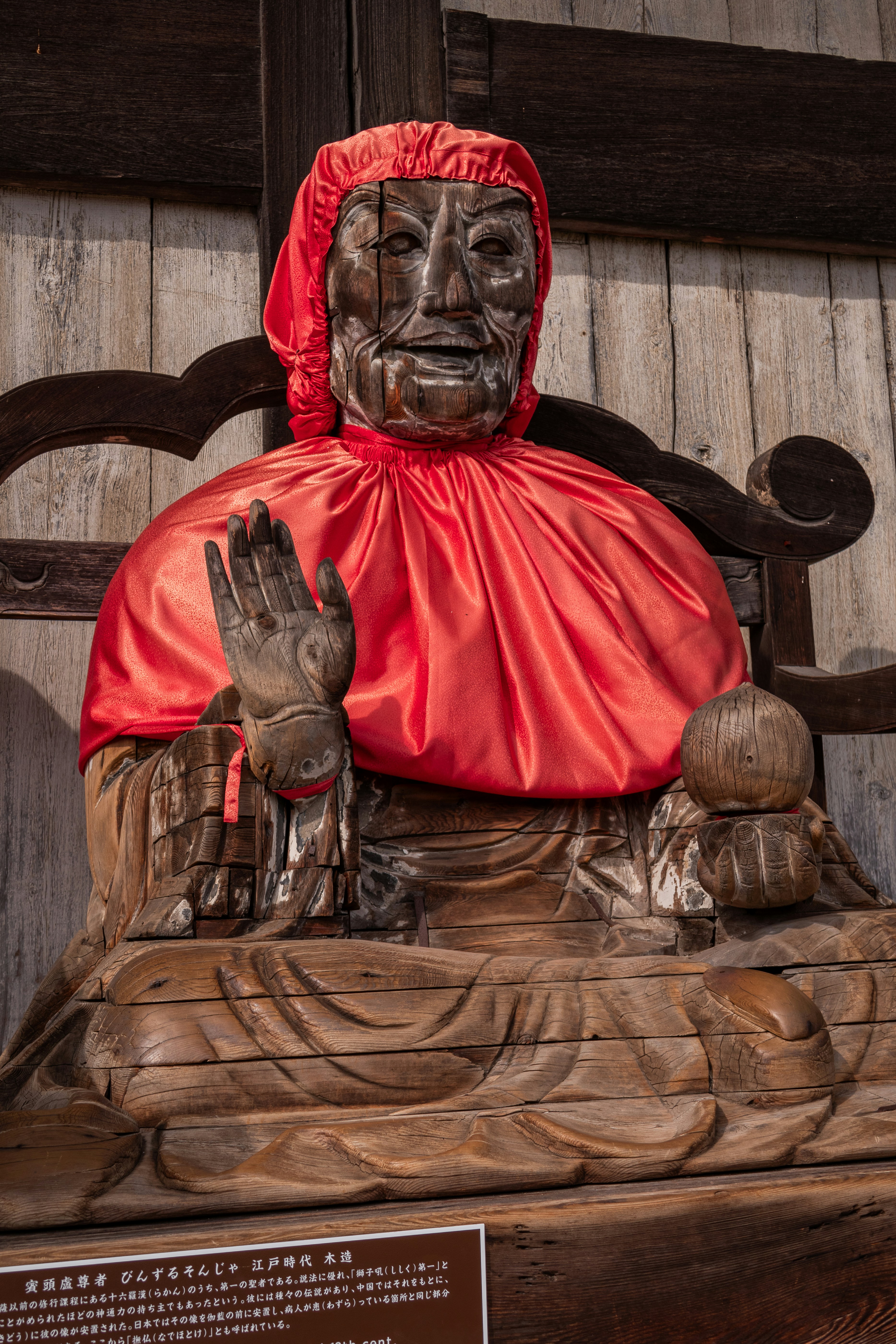 Red-robed wooden statue of a seated figure blessing with raised hand