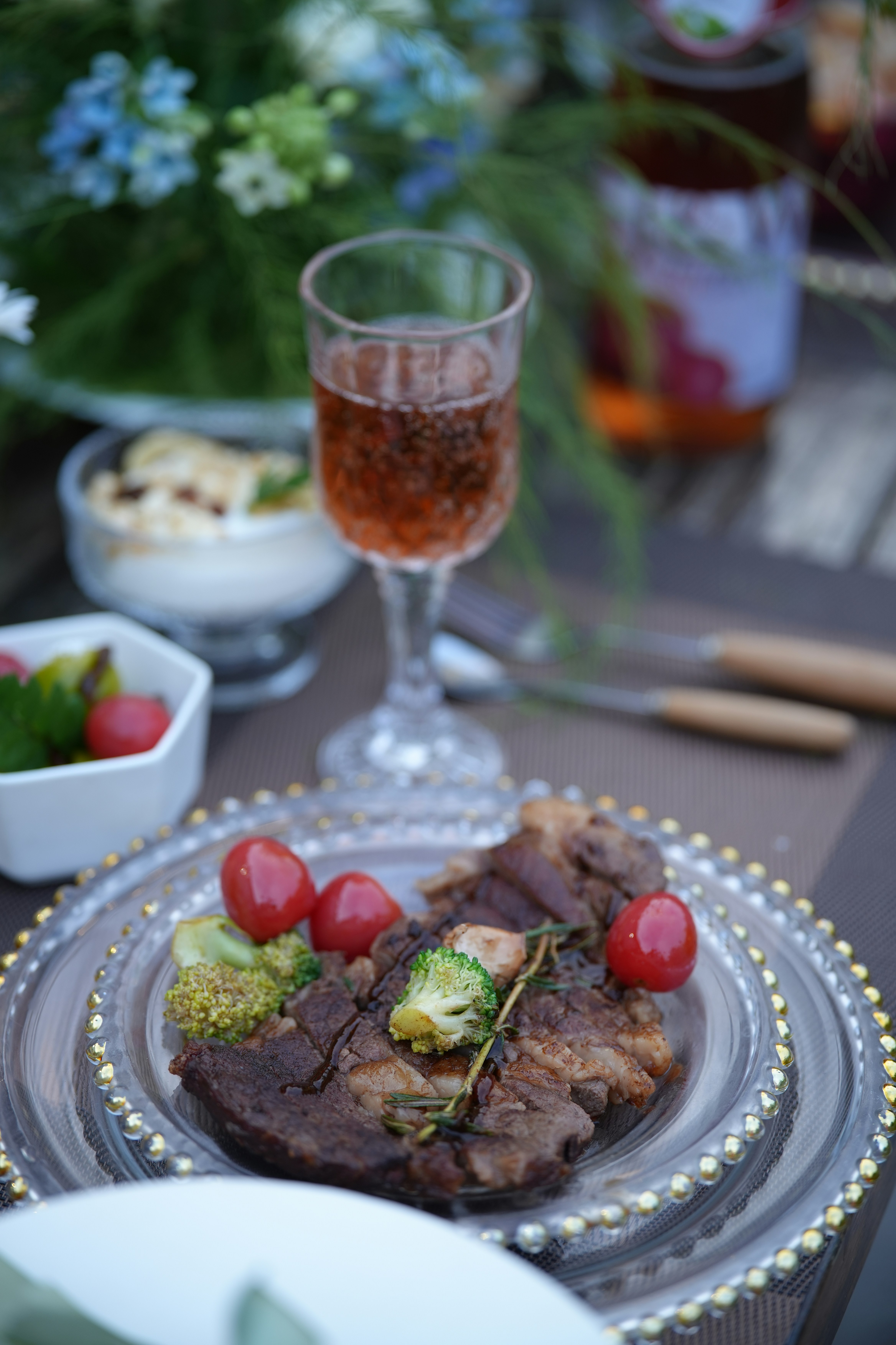 Grilled steak with tomatoes and broccoli on an outdoor table.