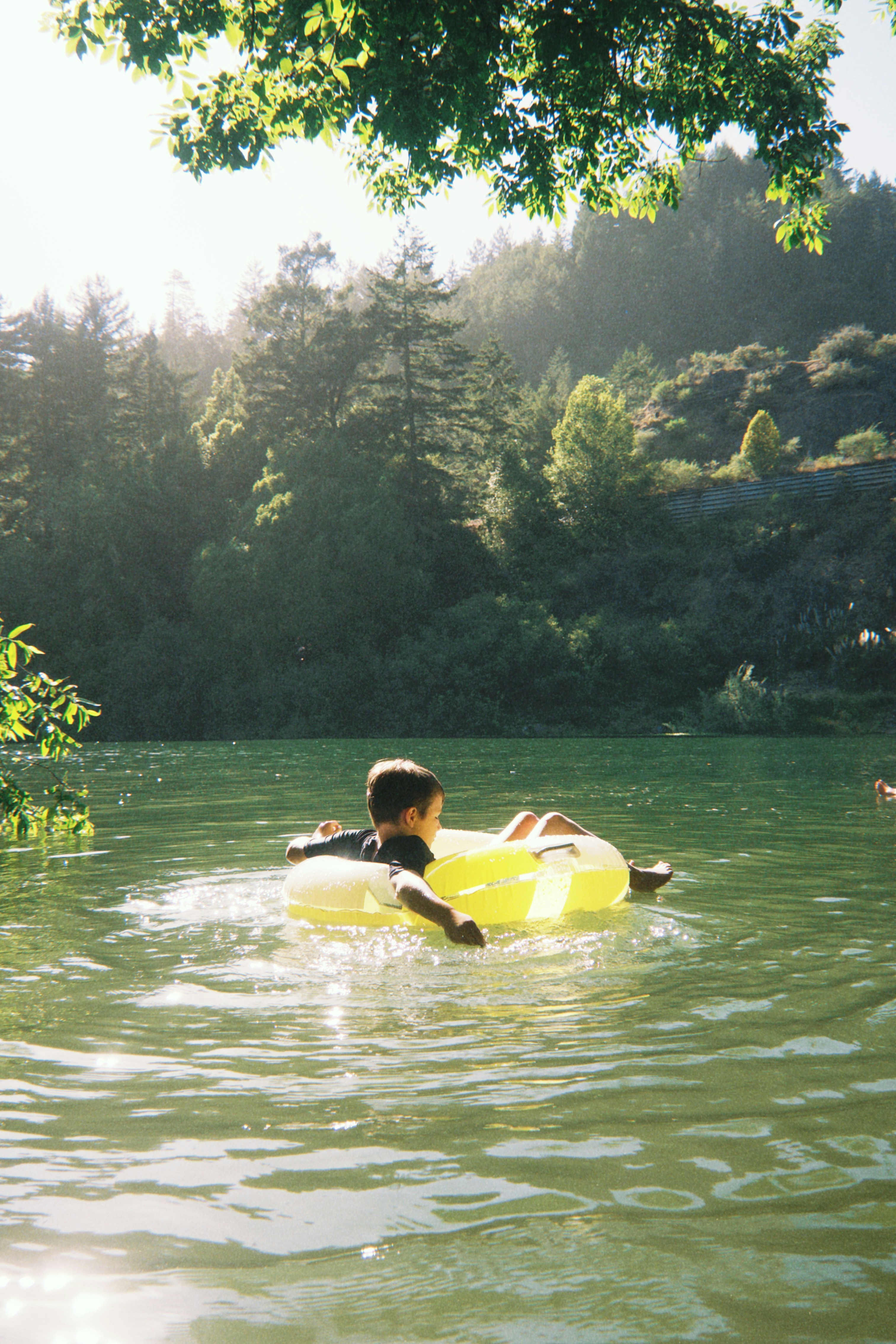 A child floats in a yellow tube on a lake.
