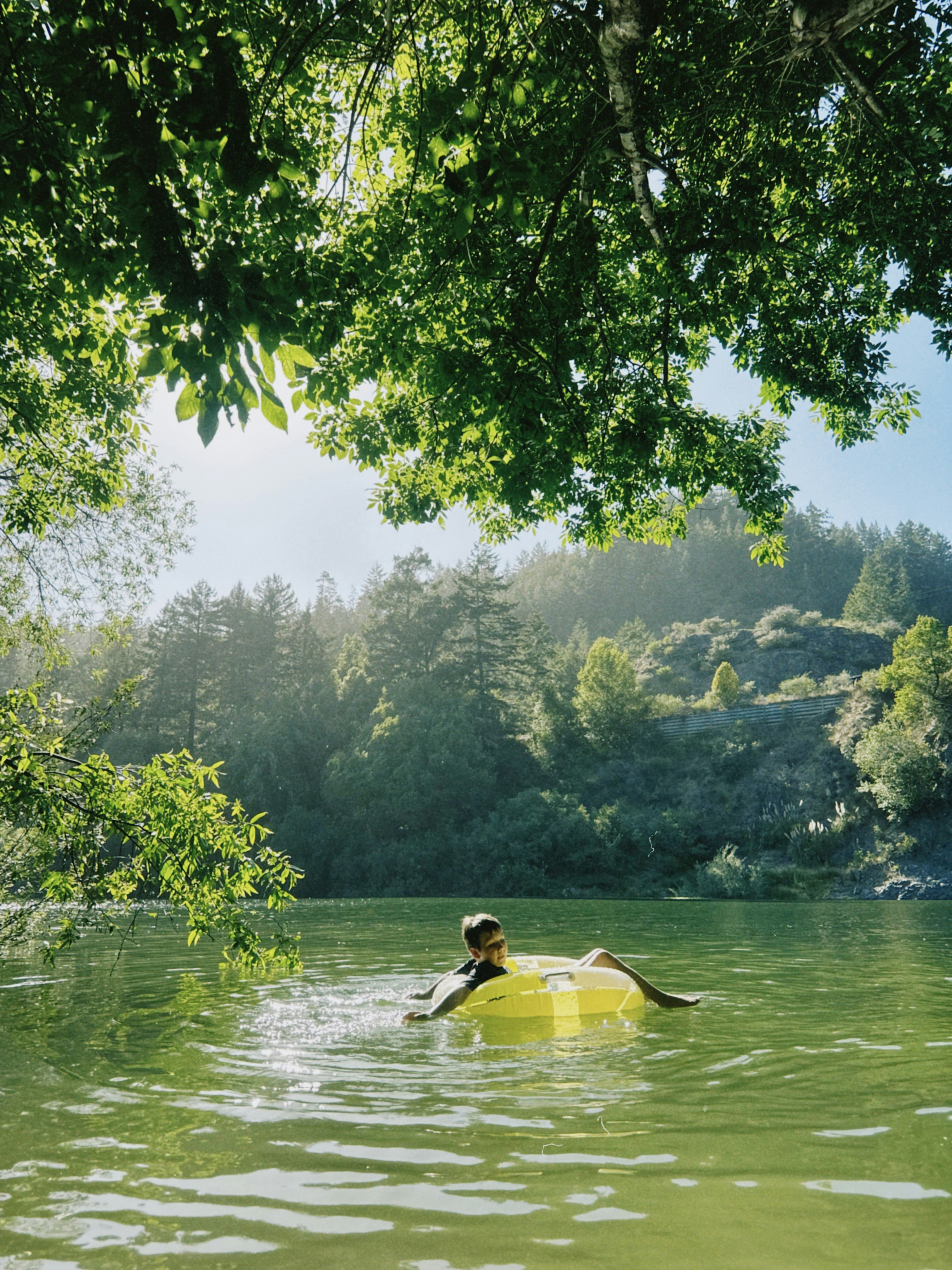 Person floating on a yellow tube in a serene lake.