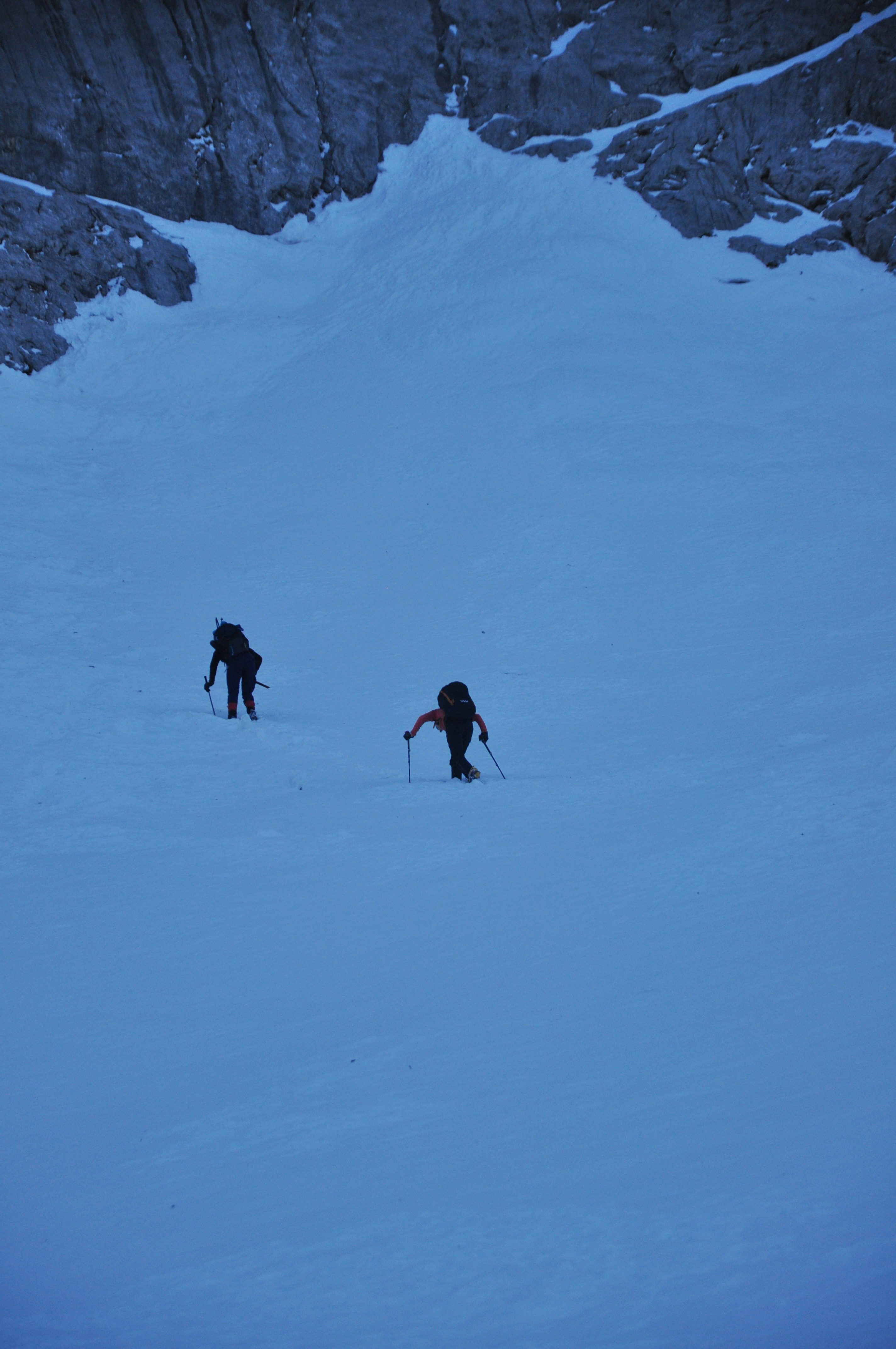 Two climbers Ascend a Steep Snowfield Beneath a Dark Ridge
