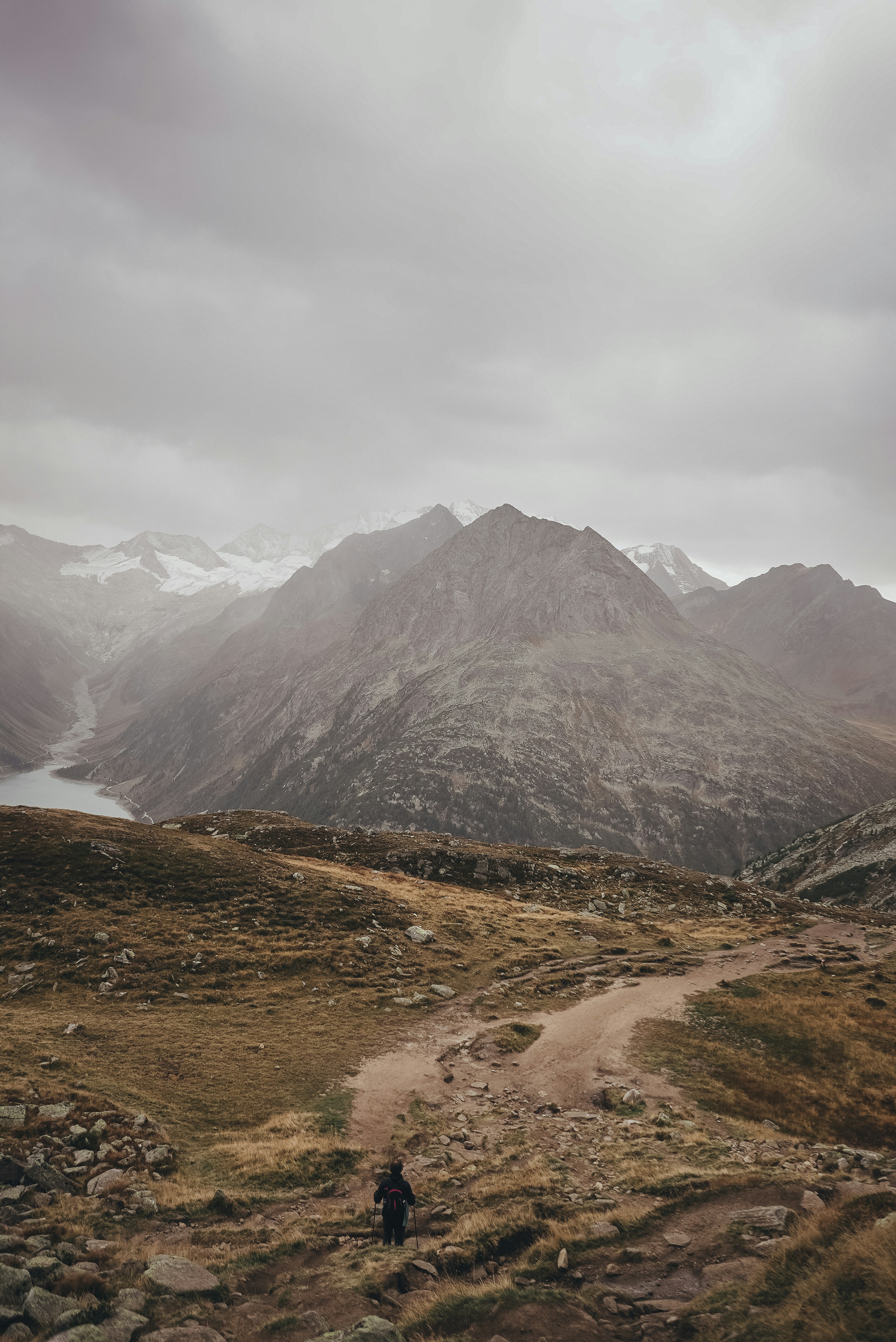 Trail toward the looming peak: a lone hiker threads a weathered pass beneath towering summits