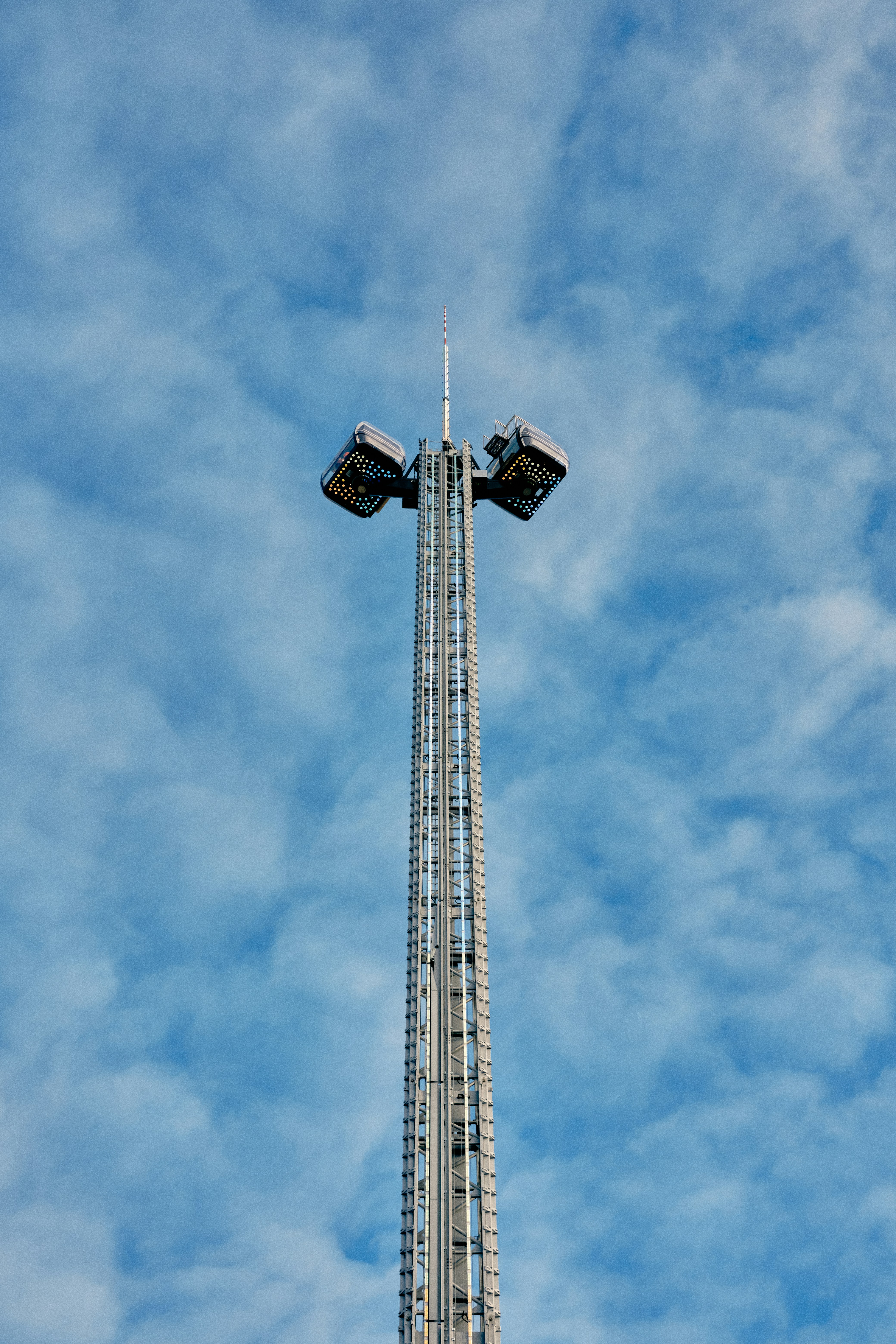 A tall drop tower ride against a cloudy blue sky.