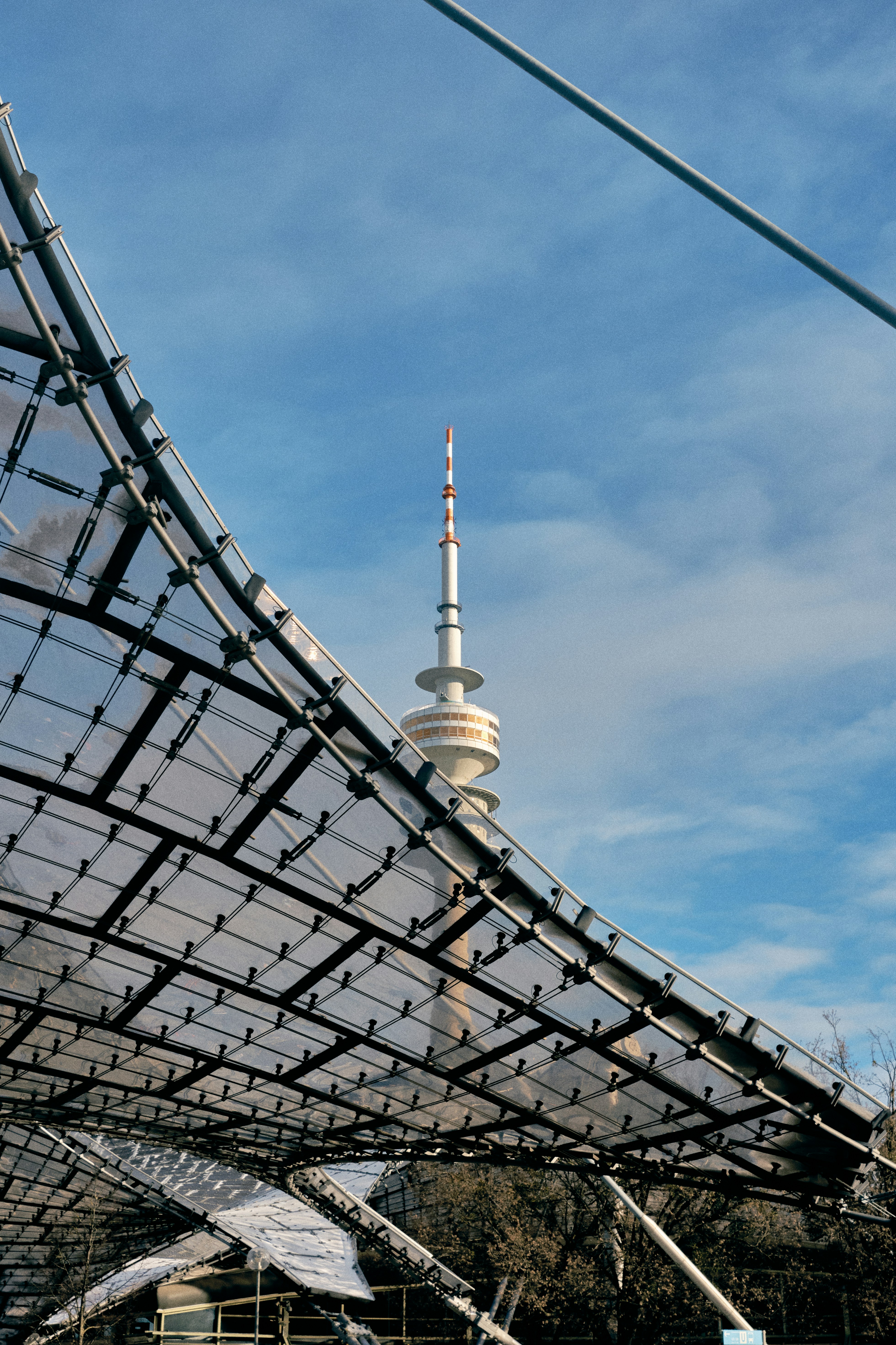 Glass canopy arcs toward the blue sky beneath a TV tower pinnacle