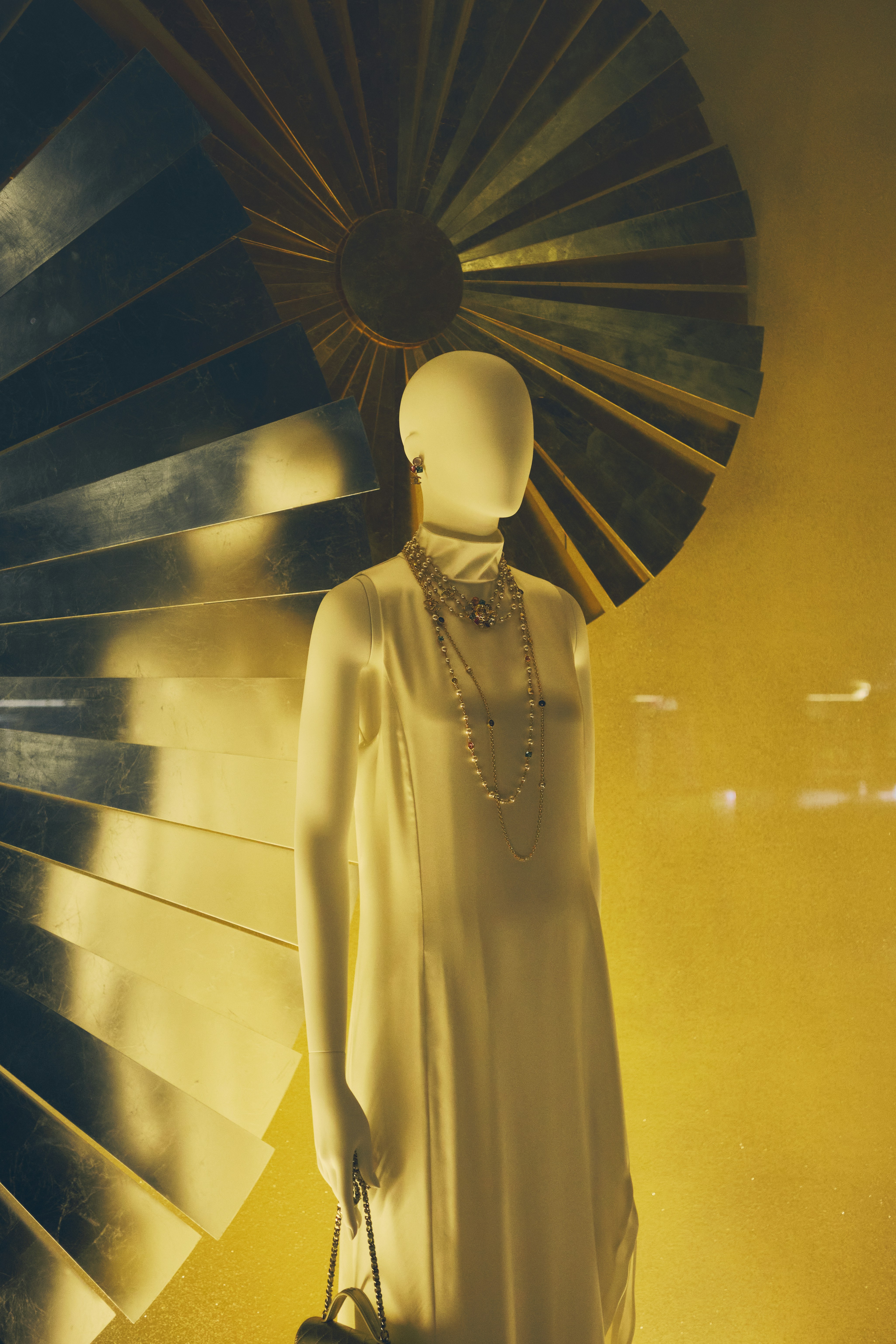 Mannequin in white dress and jewelry against a golden fan.