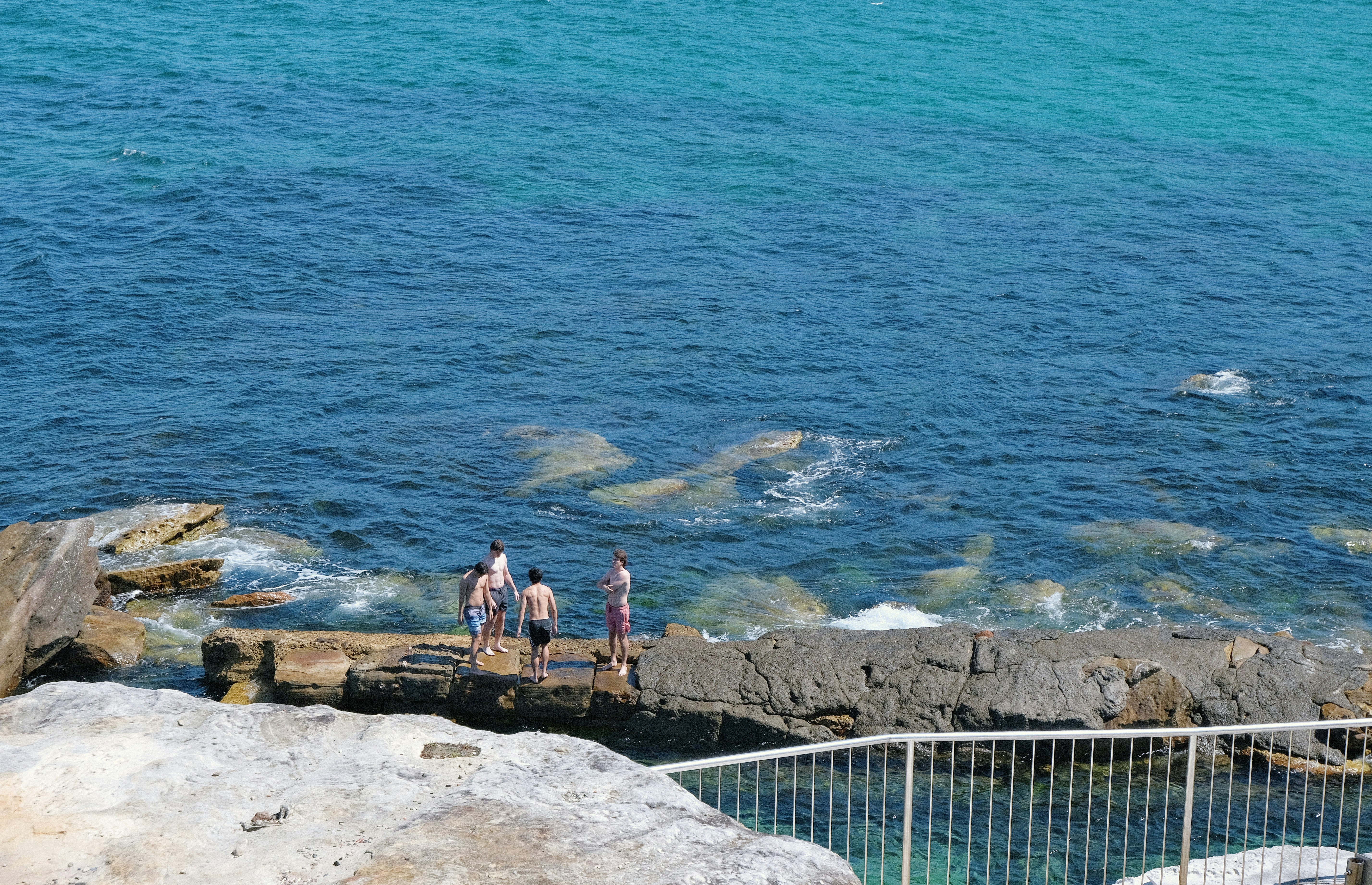 Three swimmers on a rocky jetty by clear turquoise sea