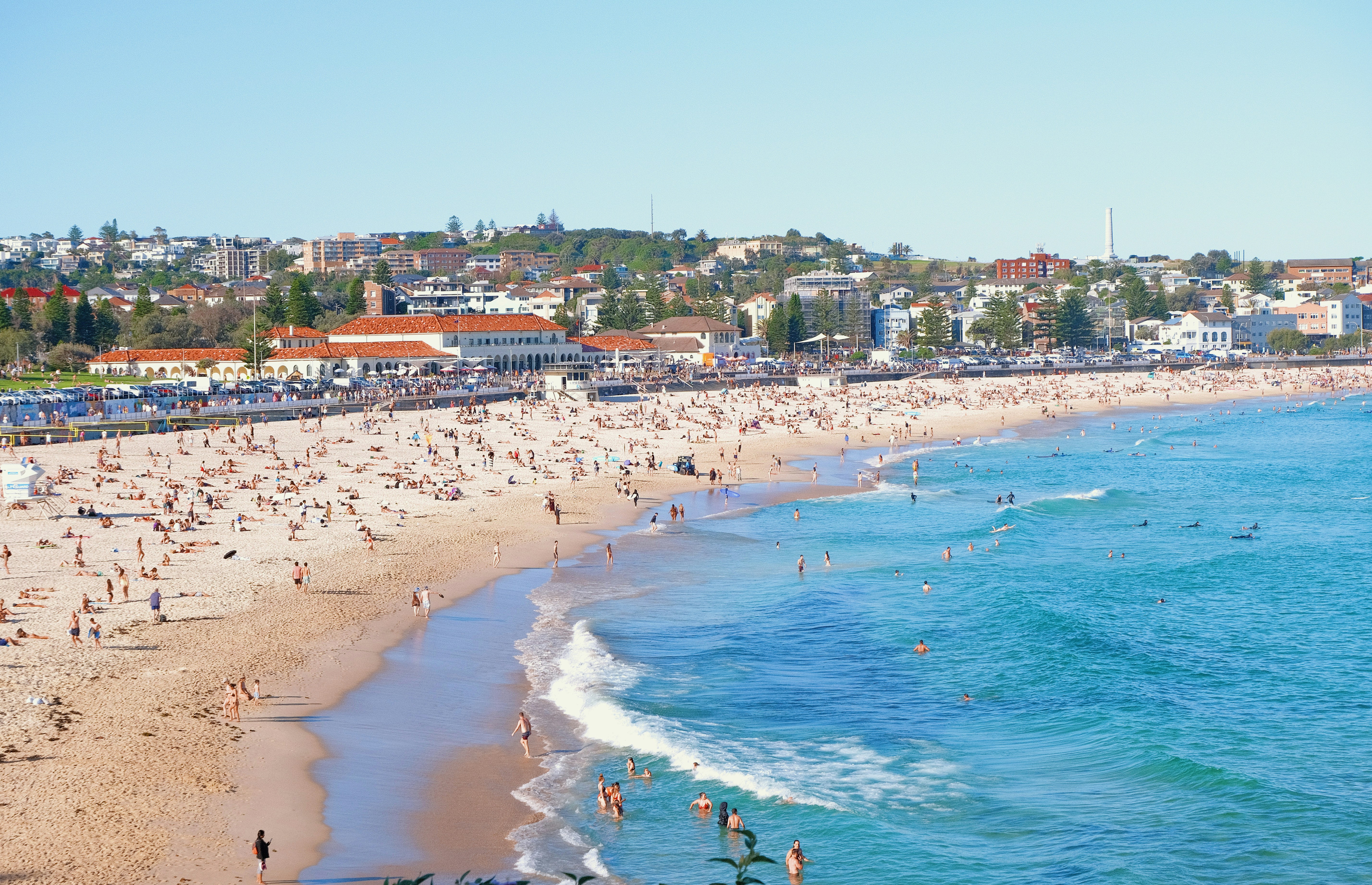 Sunlit Seaside Mosaic: People, Sand, and Surf Along a Bustling Beachfront