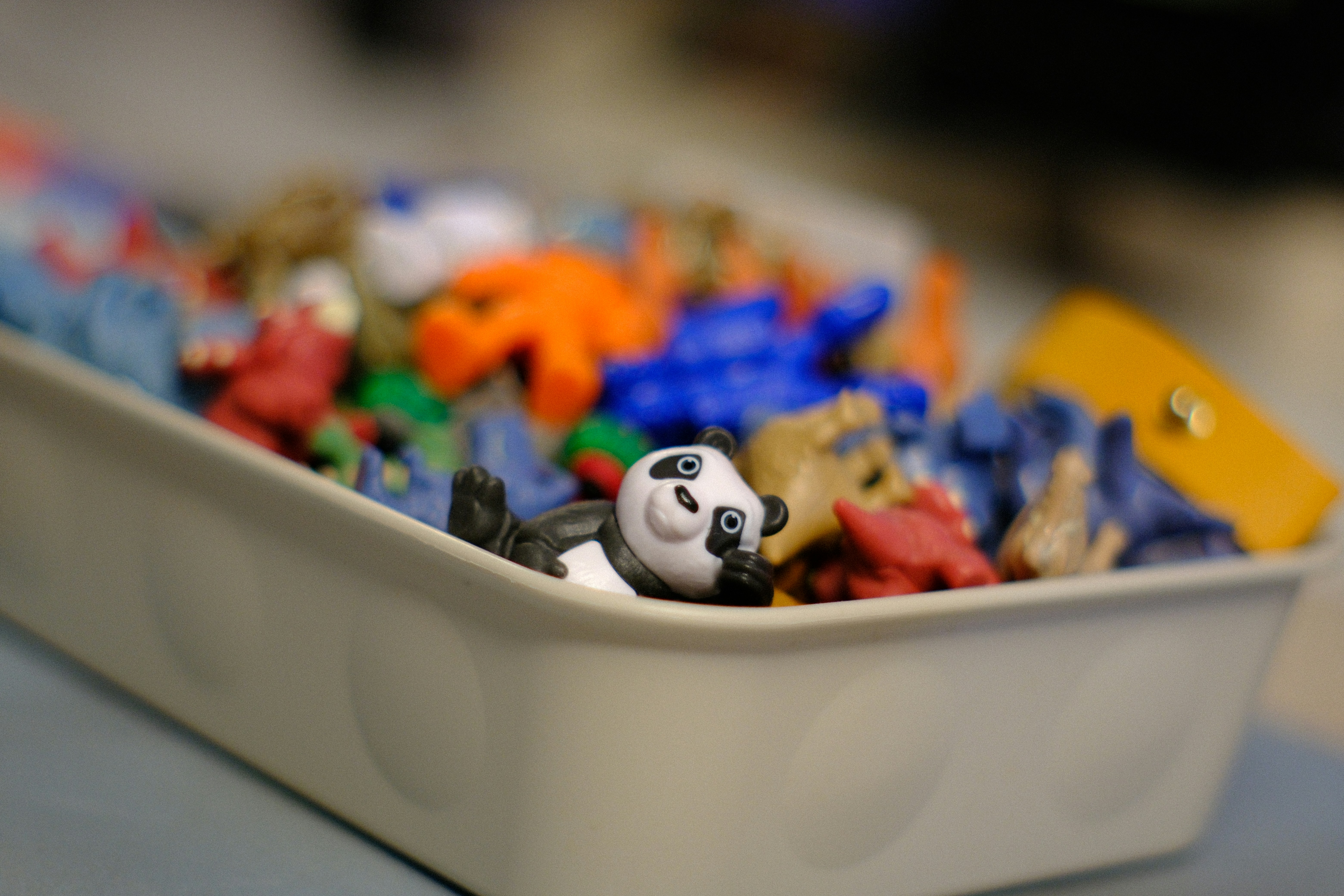 A panda figurine among colorful toys in a white container.