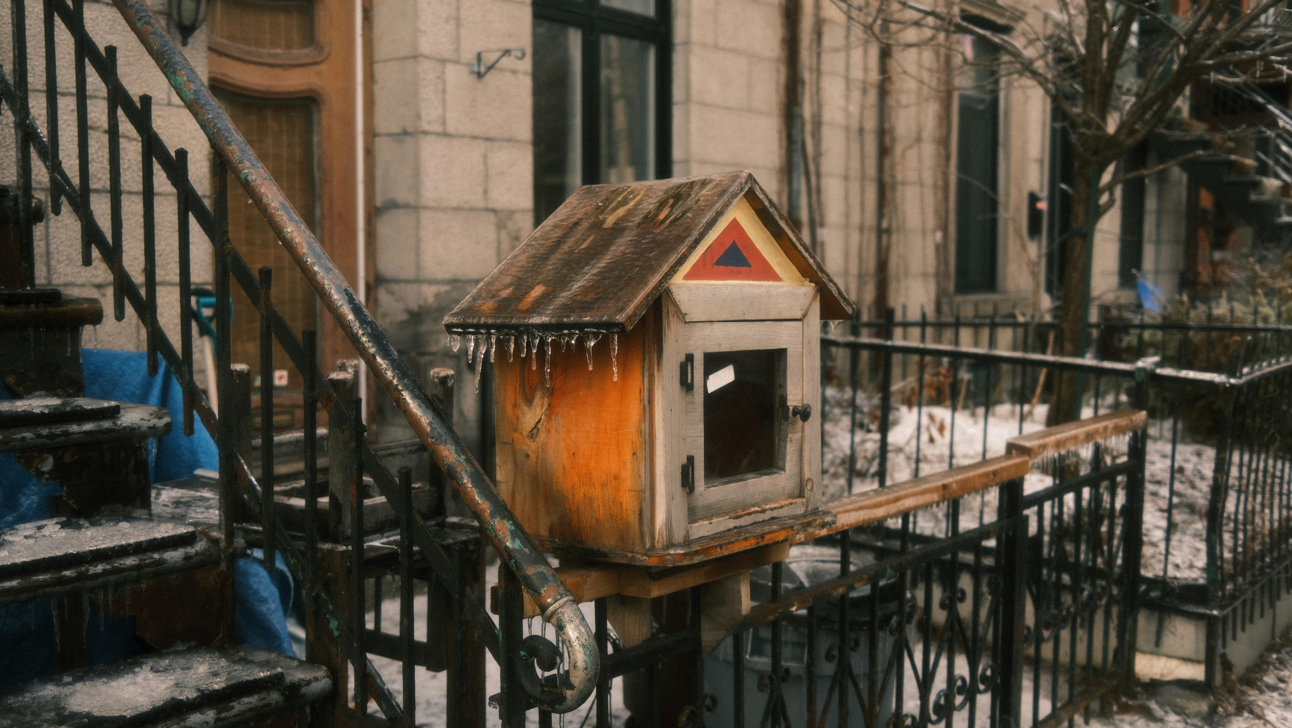 Small house-shaped box with icicles on a snowy railing.