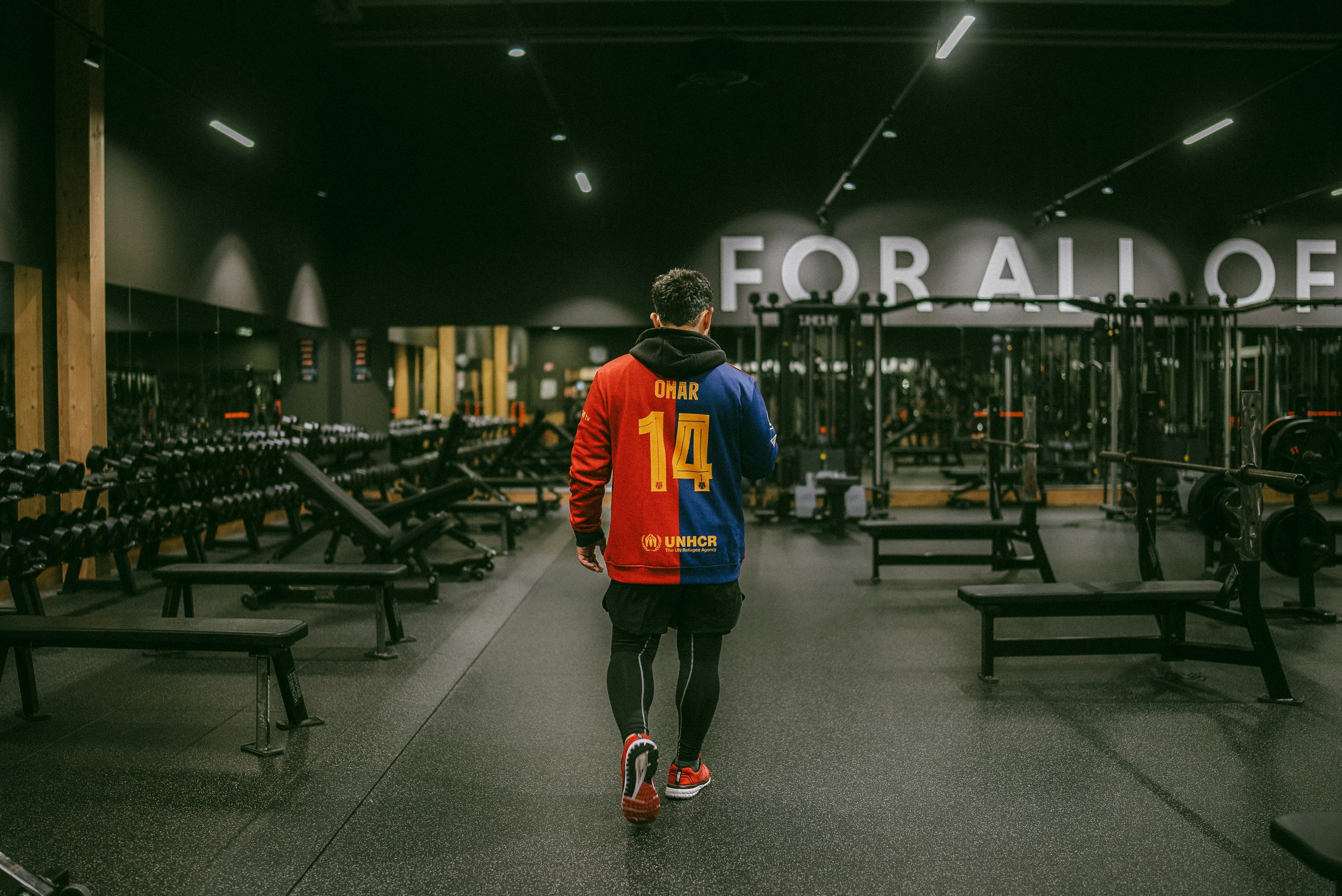 Person in a numbered jacket walks through a dark gym.