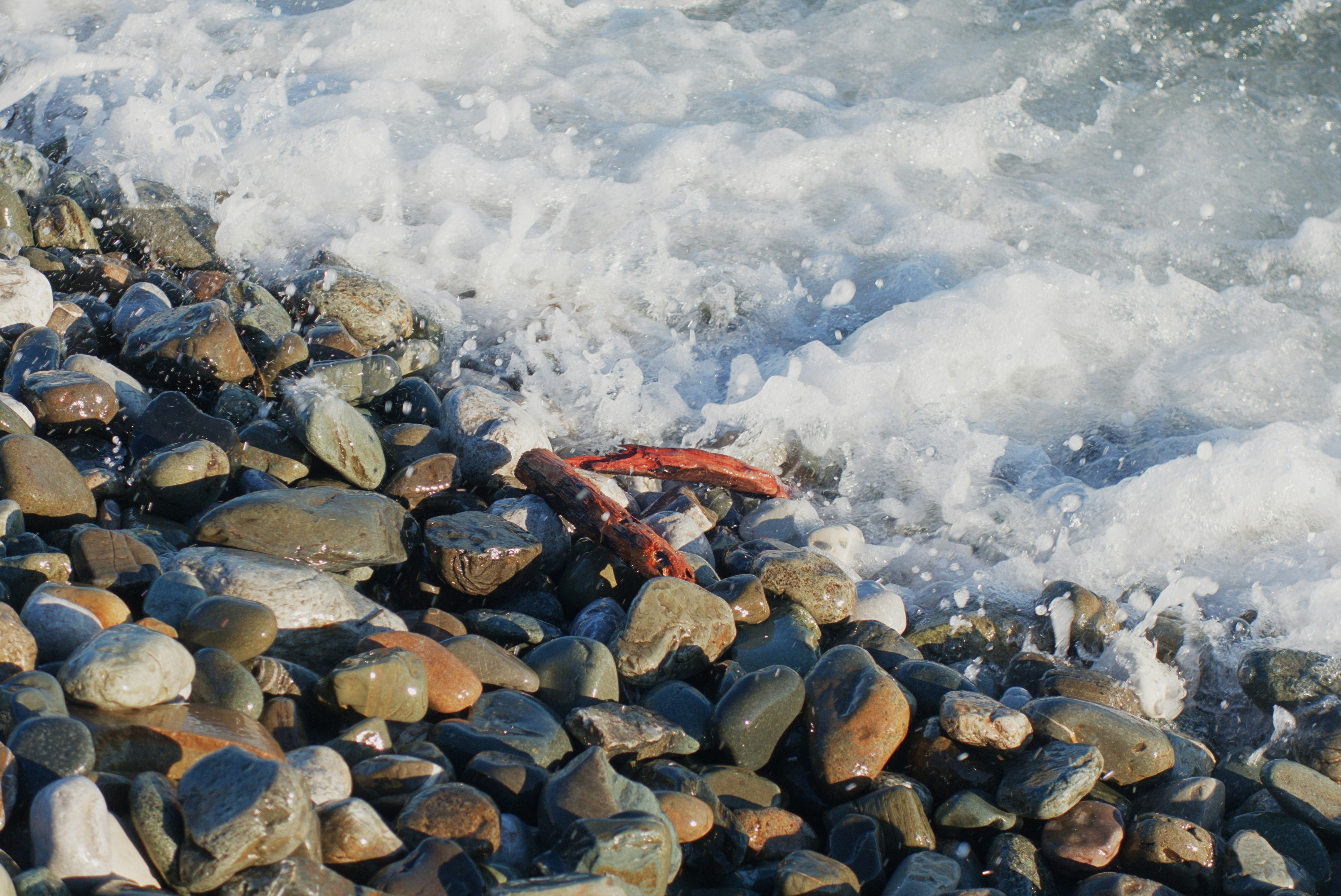Pebble shoreline kissed by sea spray with a lone orange object