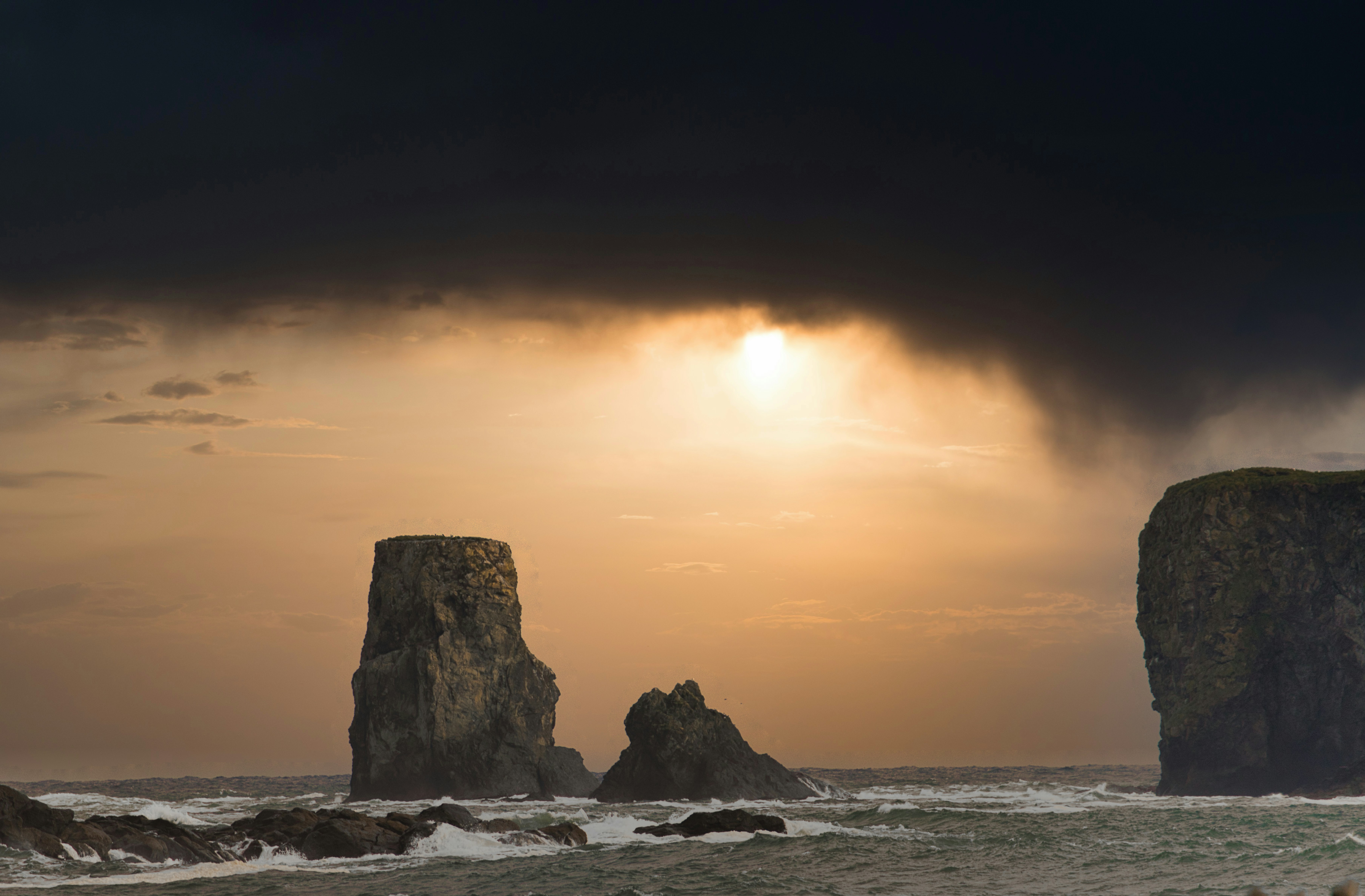 Dramatic sunset over sea stacks with dark clouds.