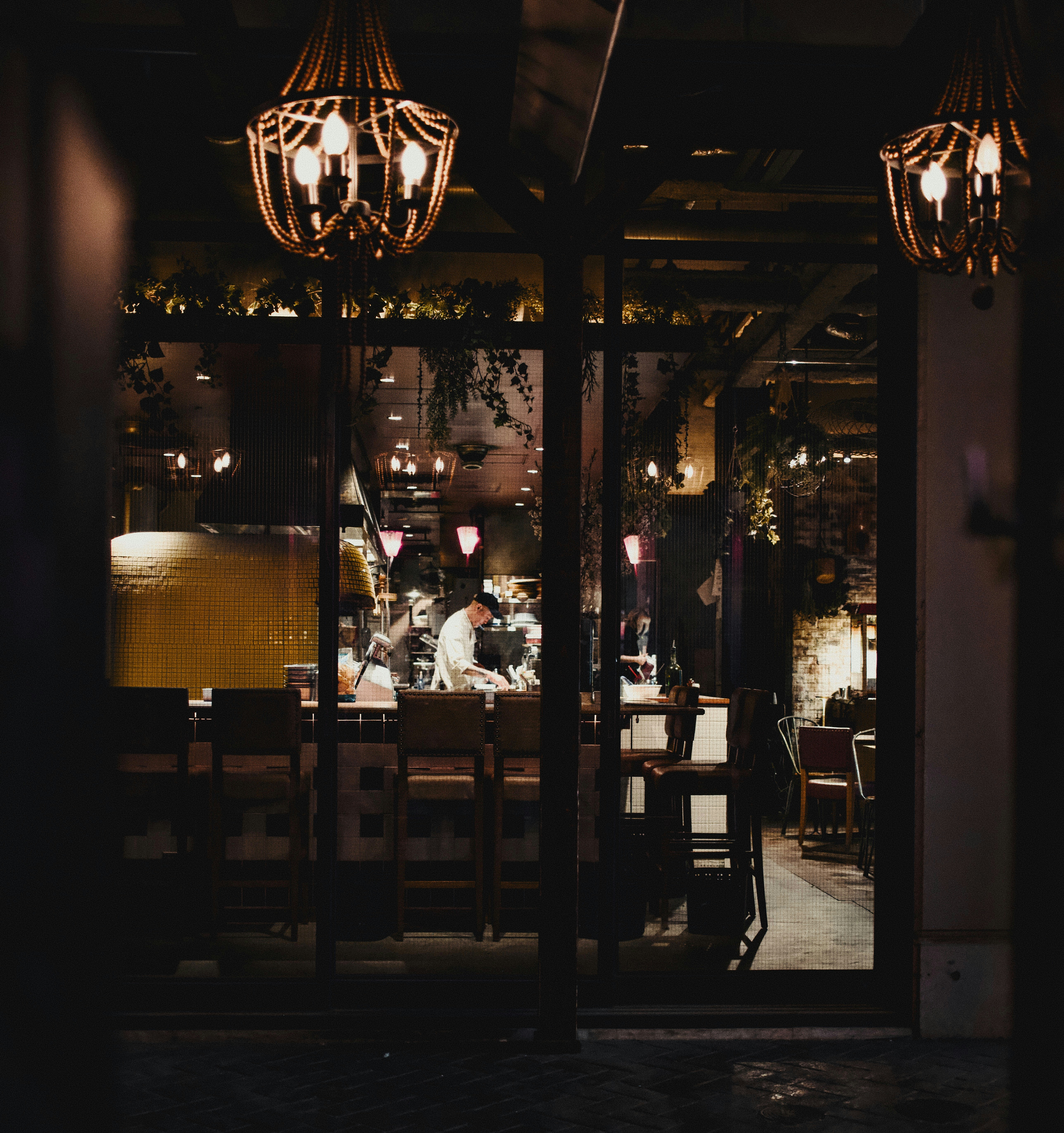 Midnight Kitchen Through Glass: Warm Lanterns and Quiet Activity