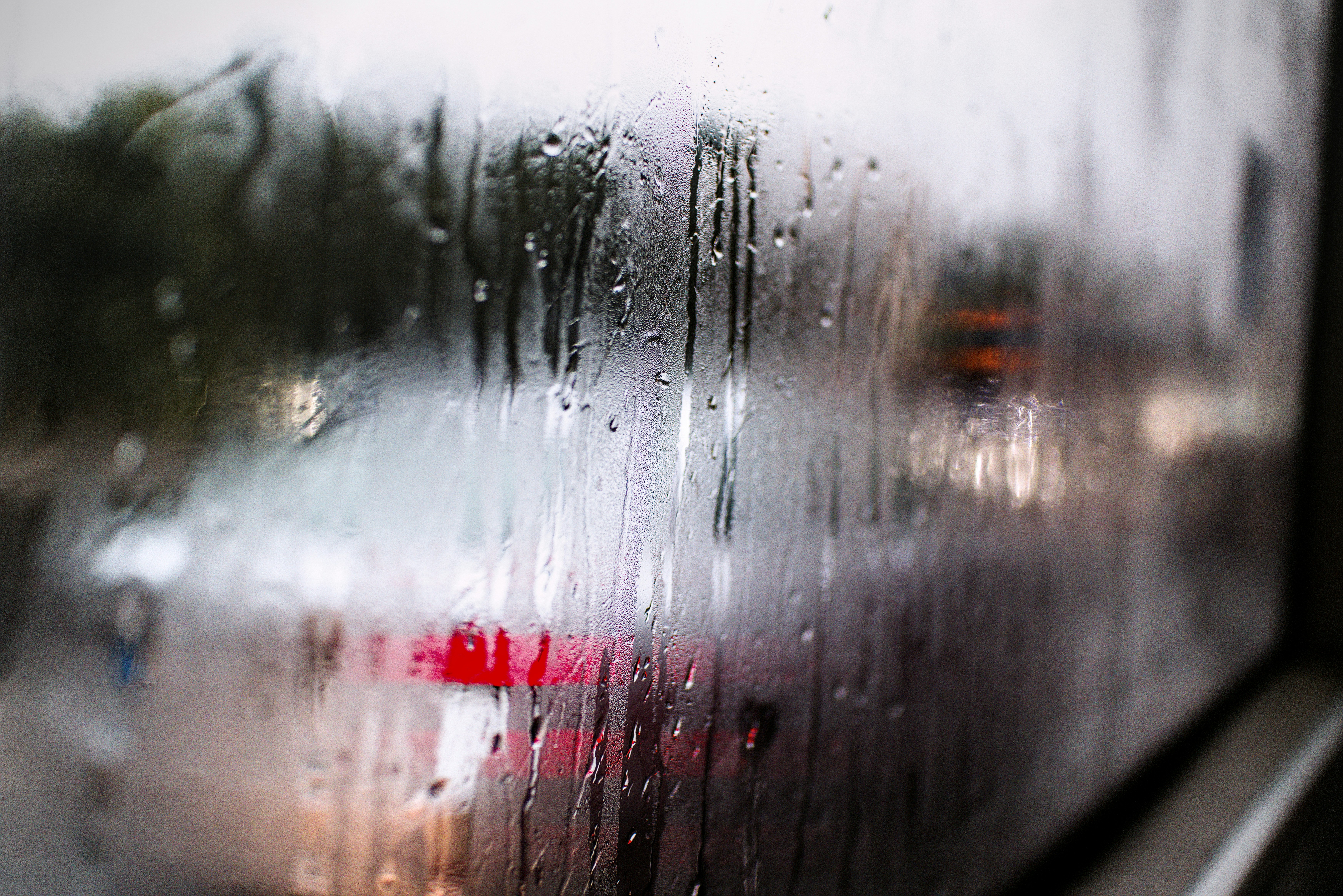 Raindrops stream down a foggy window, blurring cars outside.