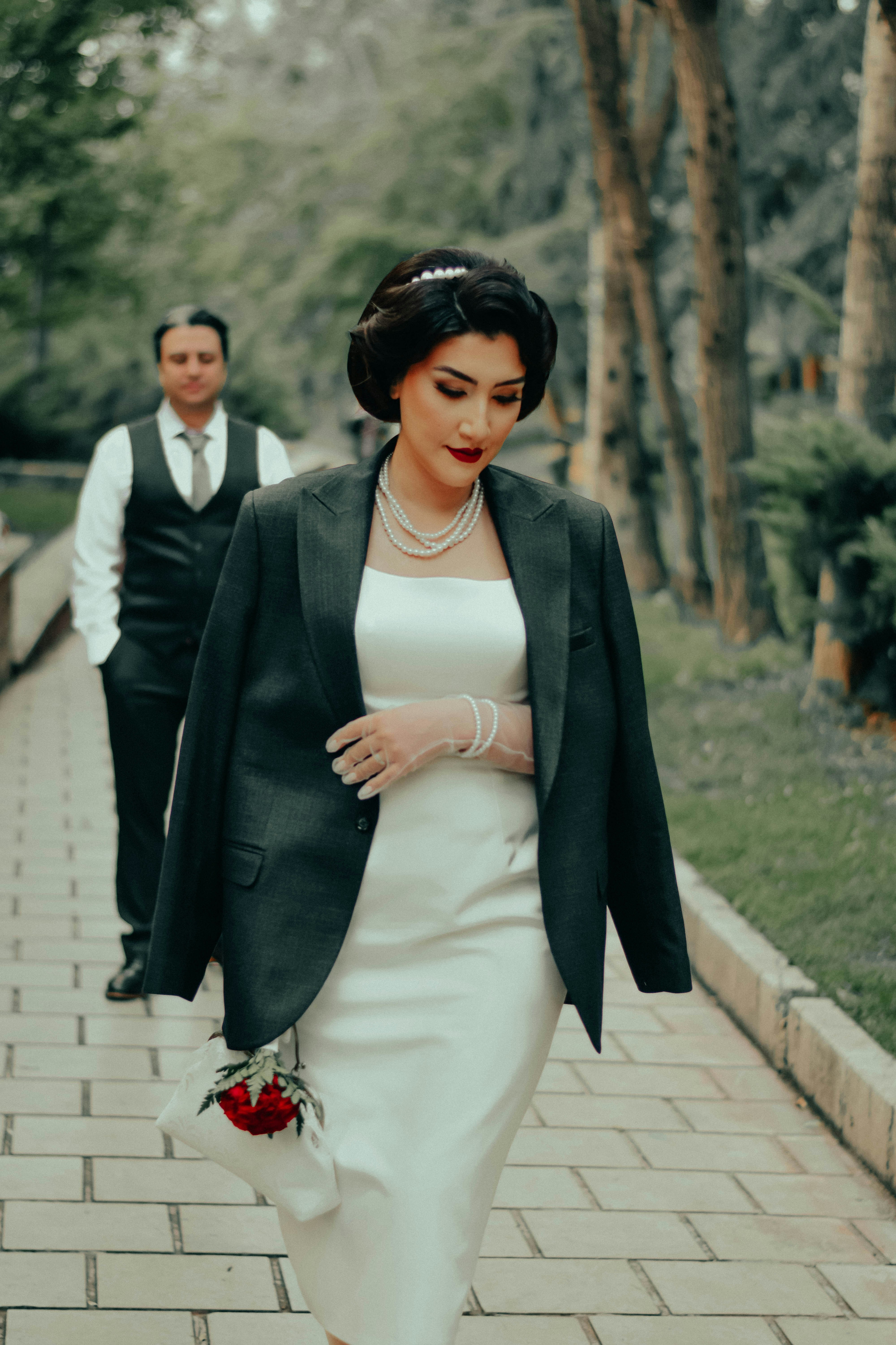 Elegant Bride in a Dark Blazer Walks Down a Garden Path