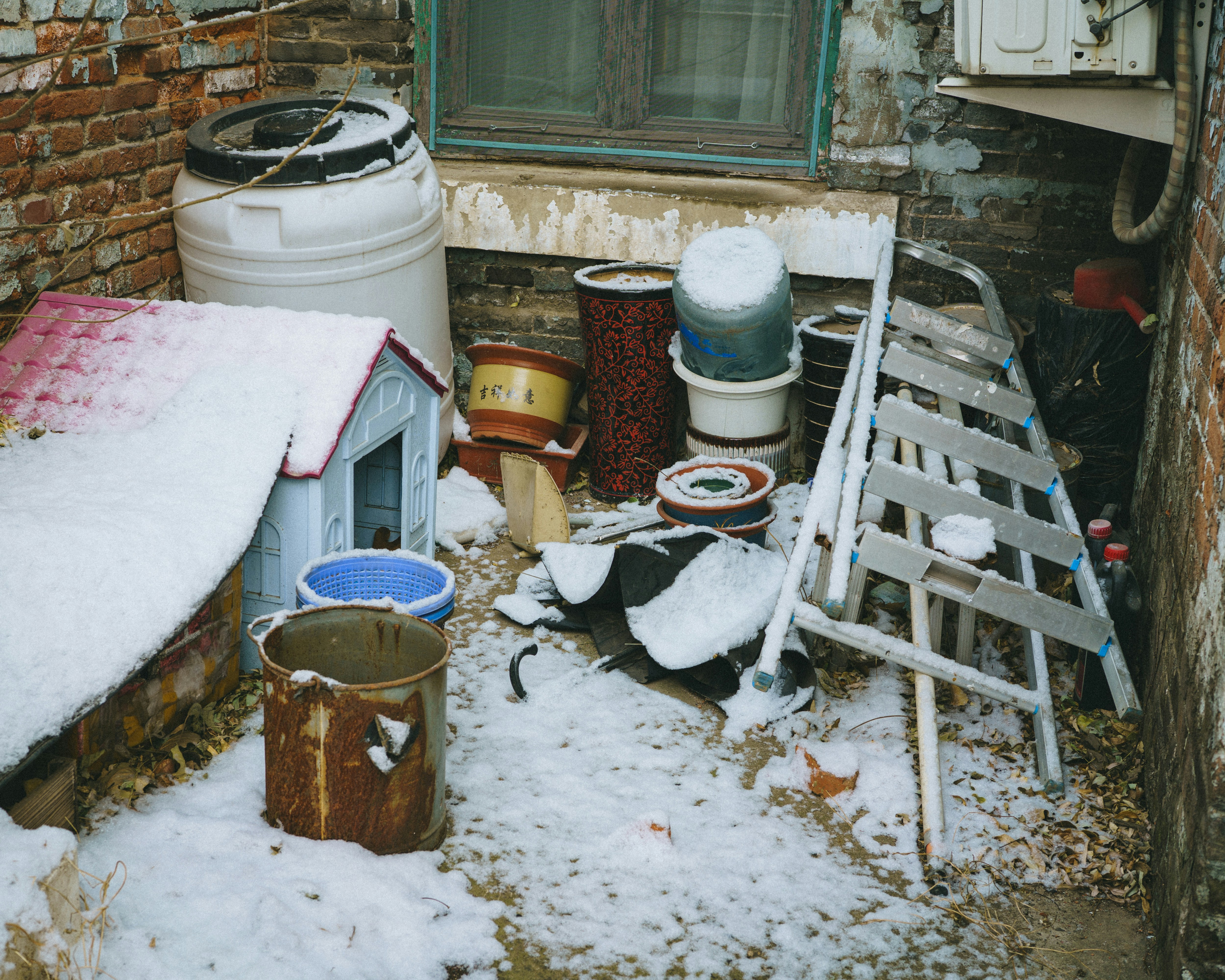 Snow-dusted clutter and makeshift courtyard in a cramped alleyway