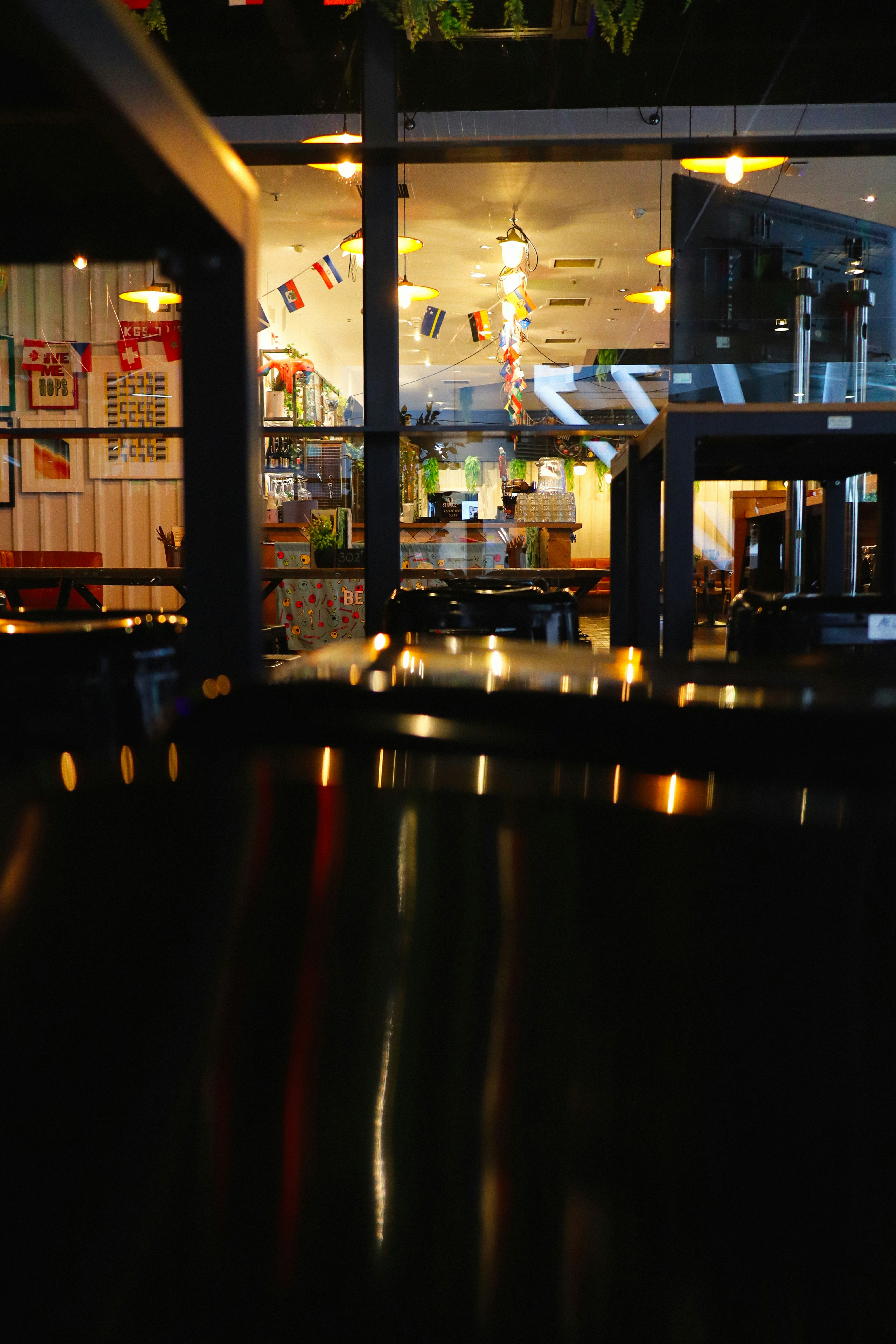 Interior of a warmly lit cafe with hanging lamps, flags, and shelves framed by dark foreground reflections.