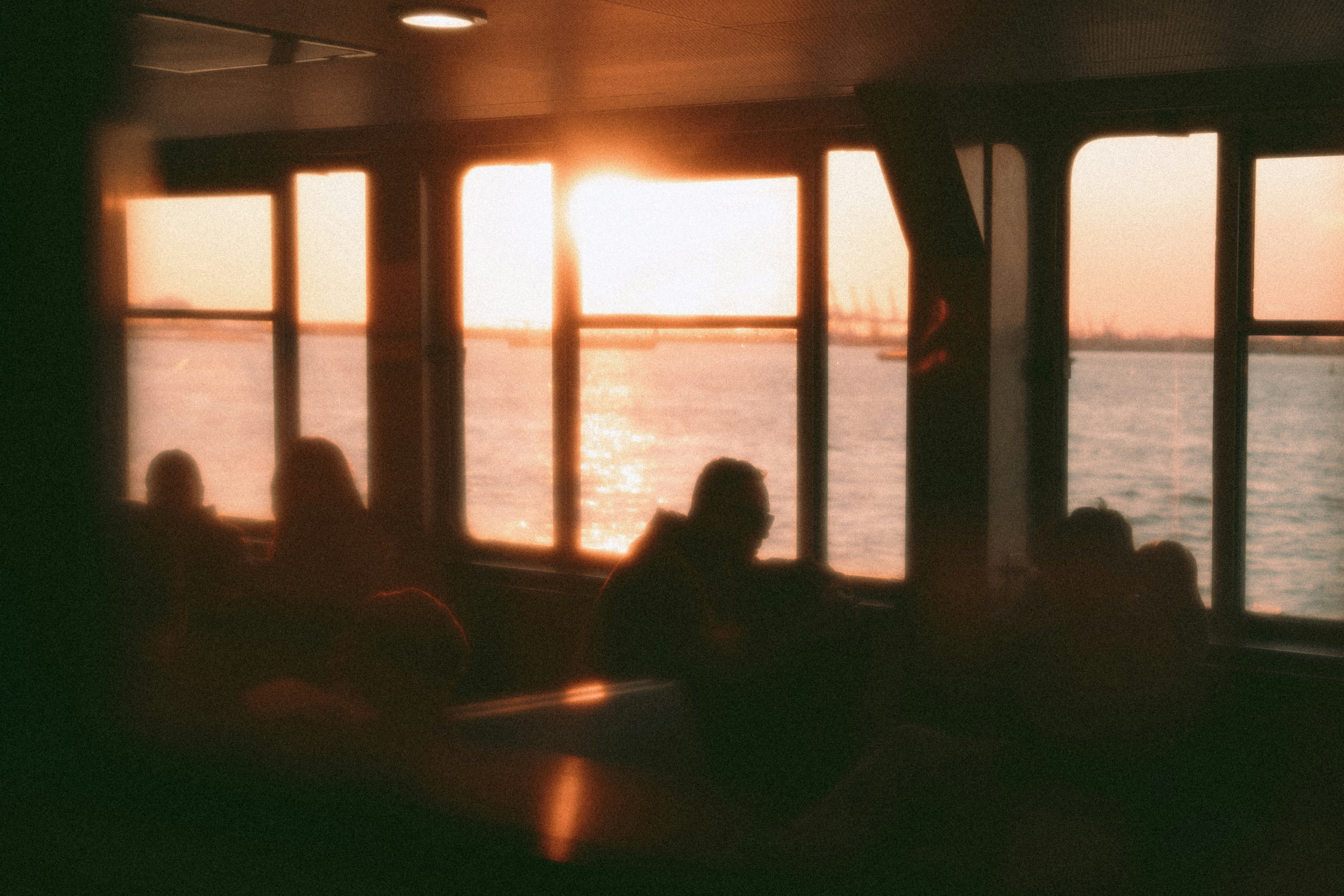 Sunlit silhouettes aboard a dim ferry as windows glow with the harbor light